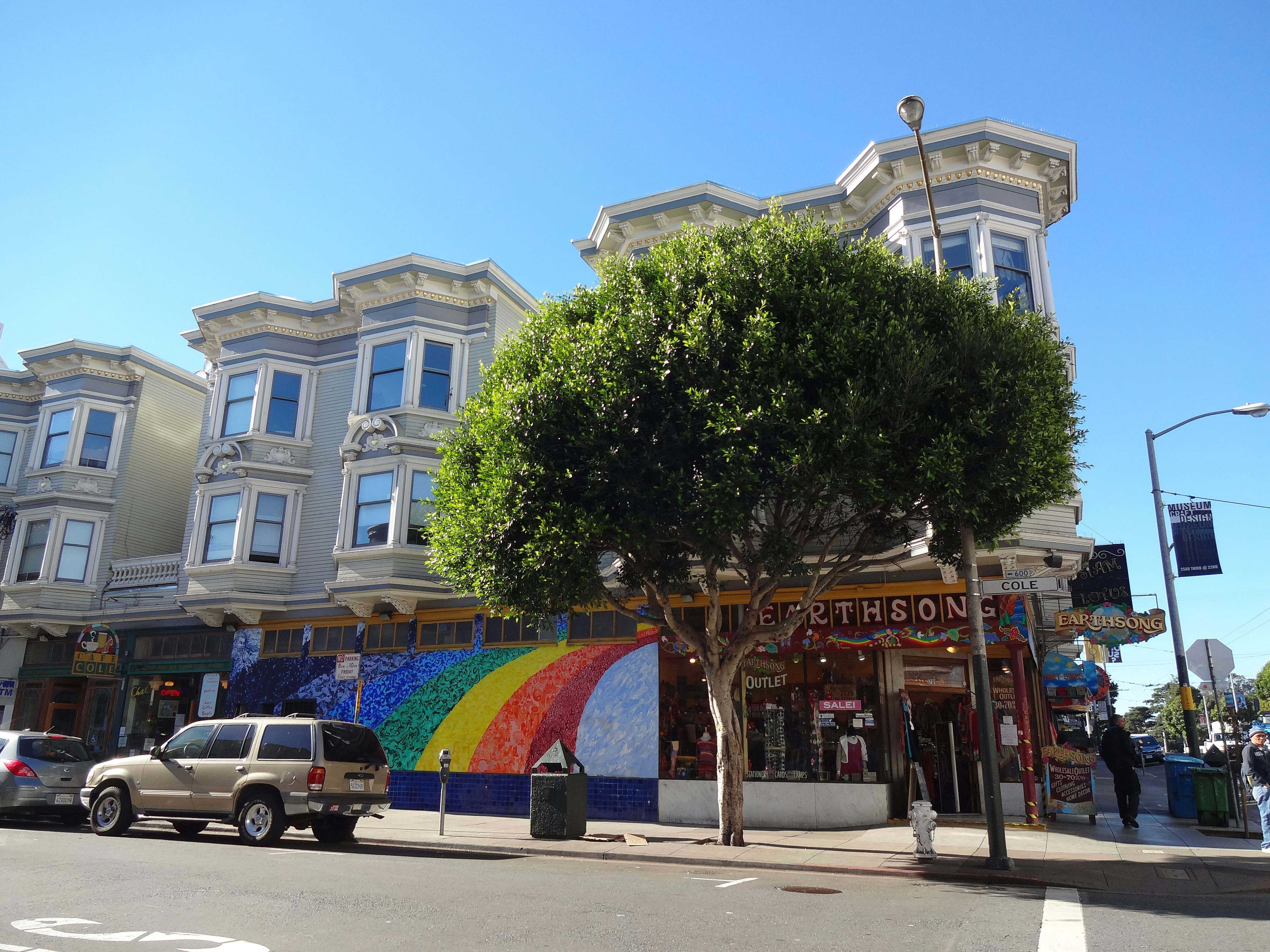 Buildings with rainbow mural and tree on street.