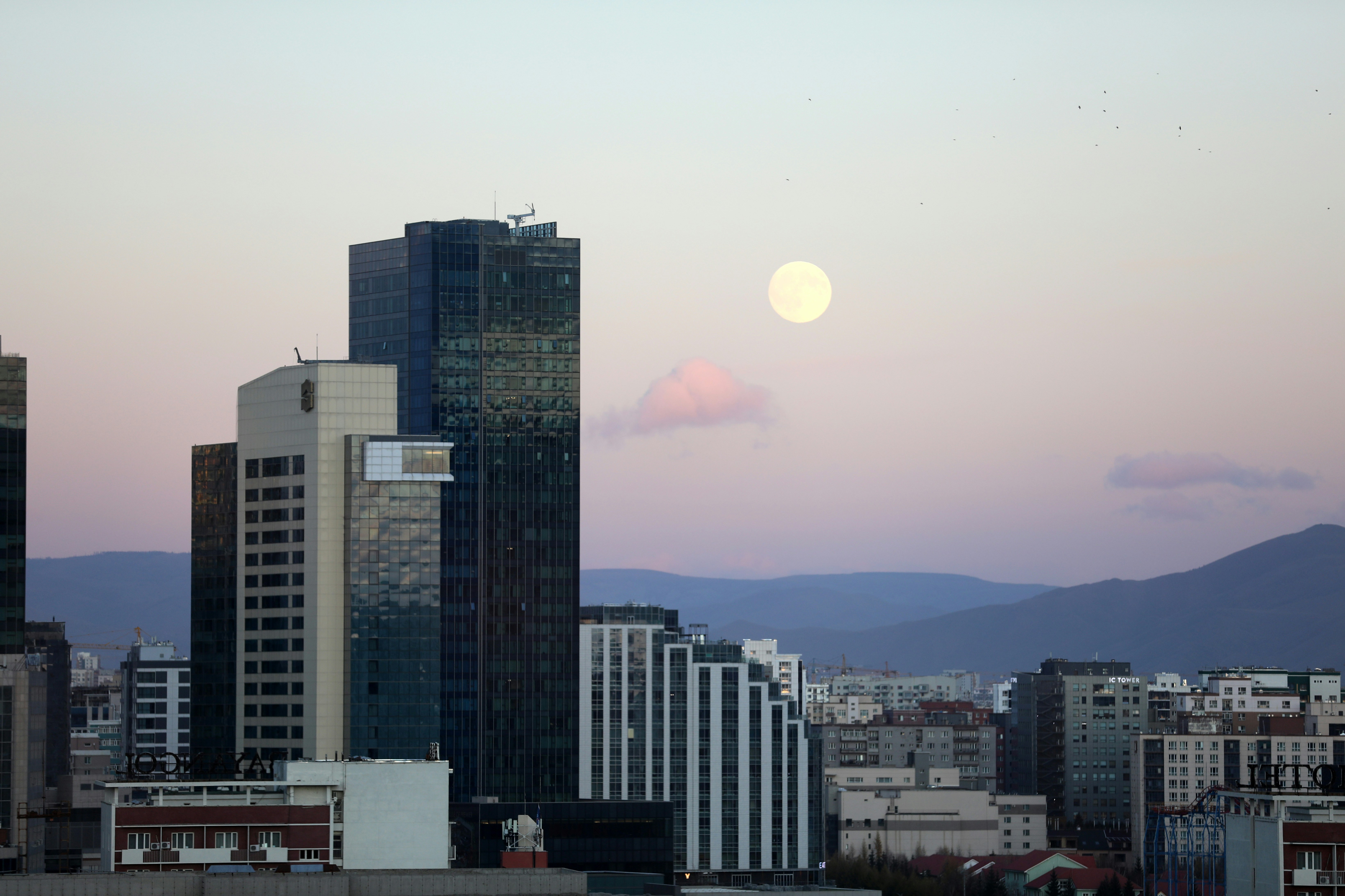 Full moon rises over a city skyline at dusk