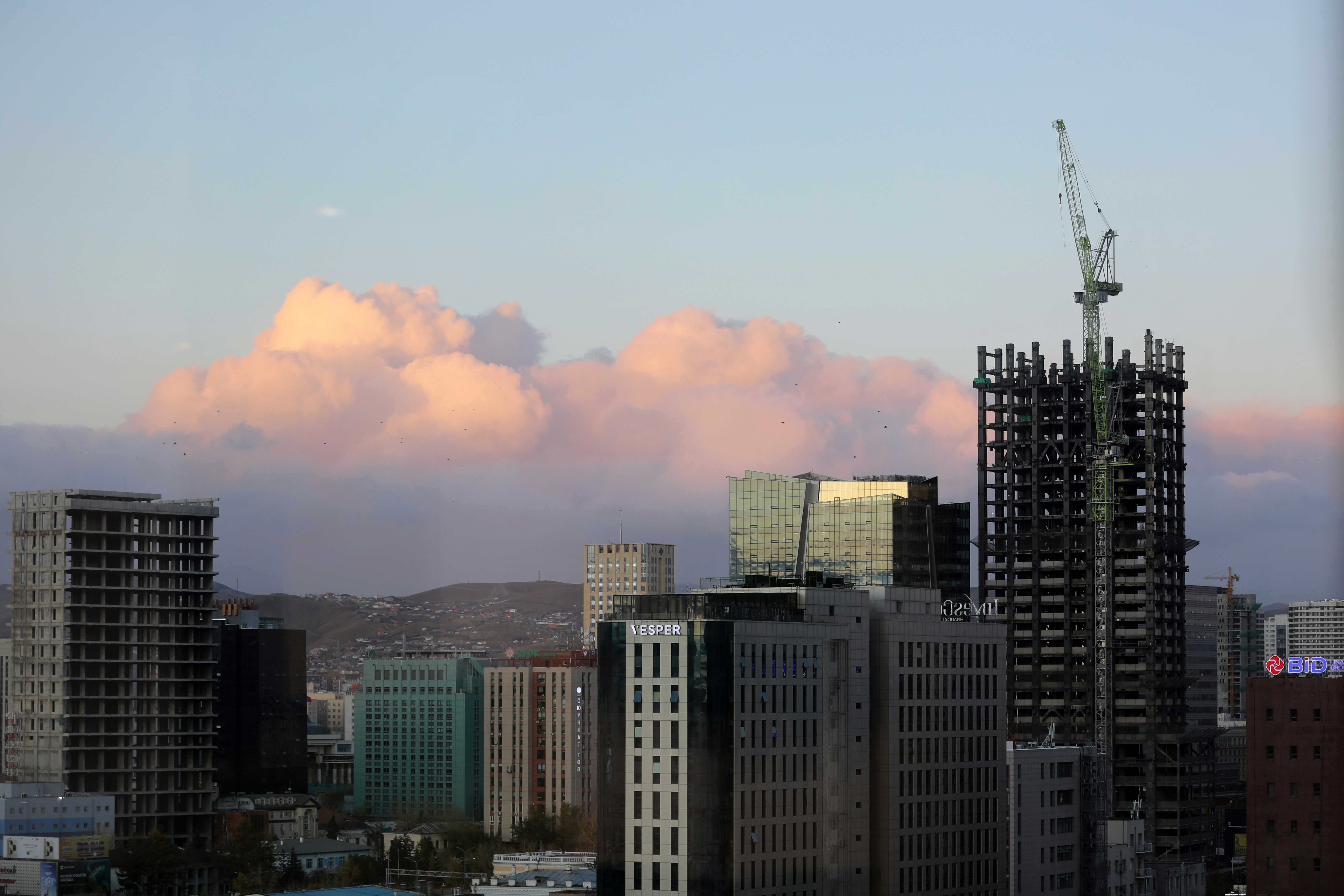 City skyline with construction and pink clouds at dusk.
