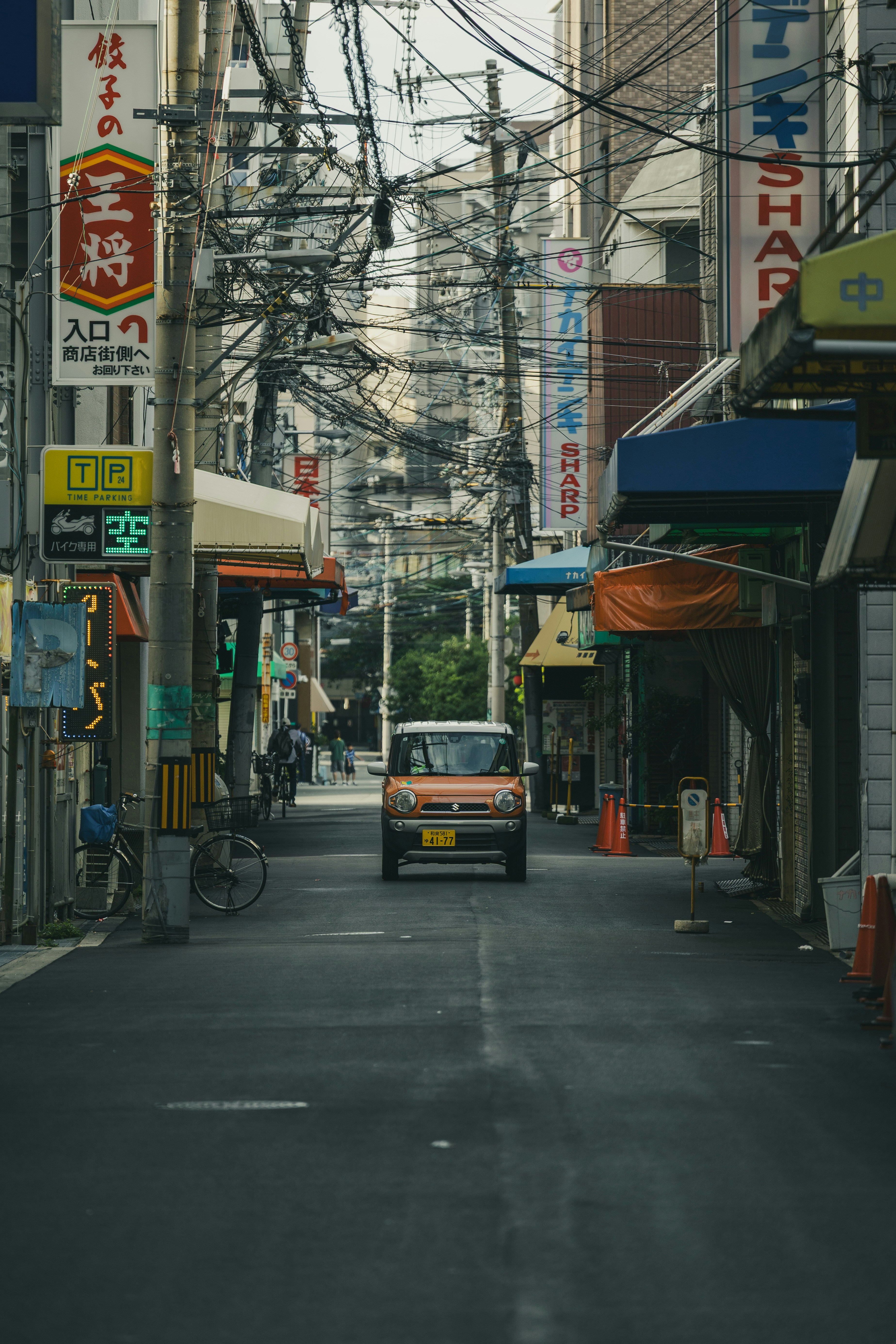Orange car drives down a narrow city street.
