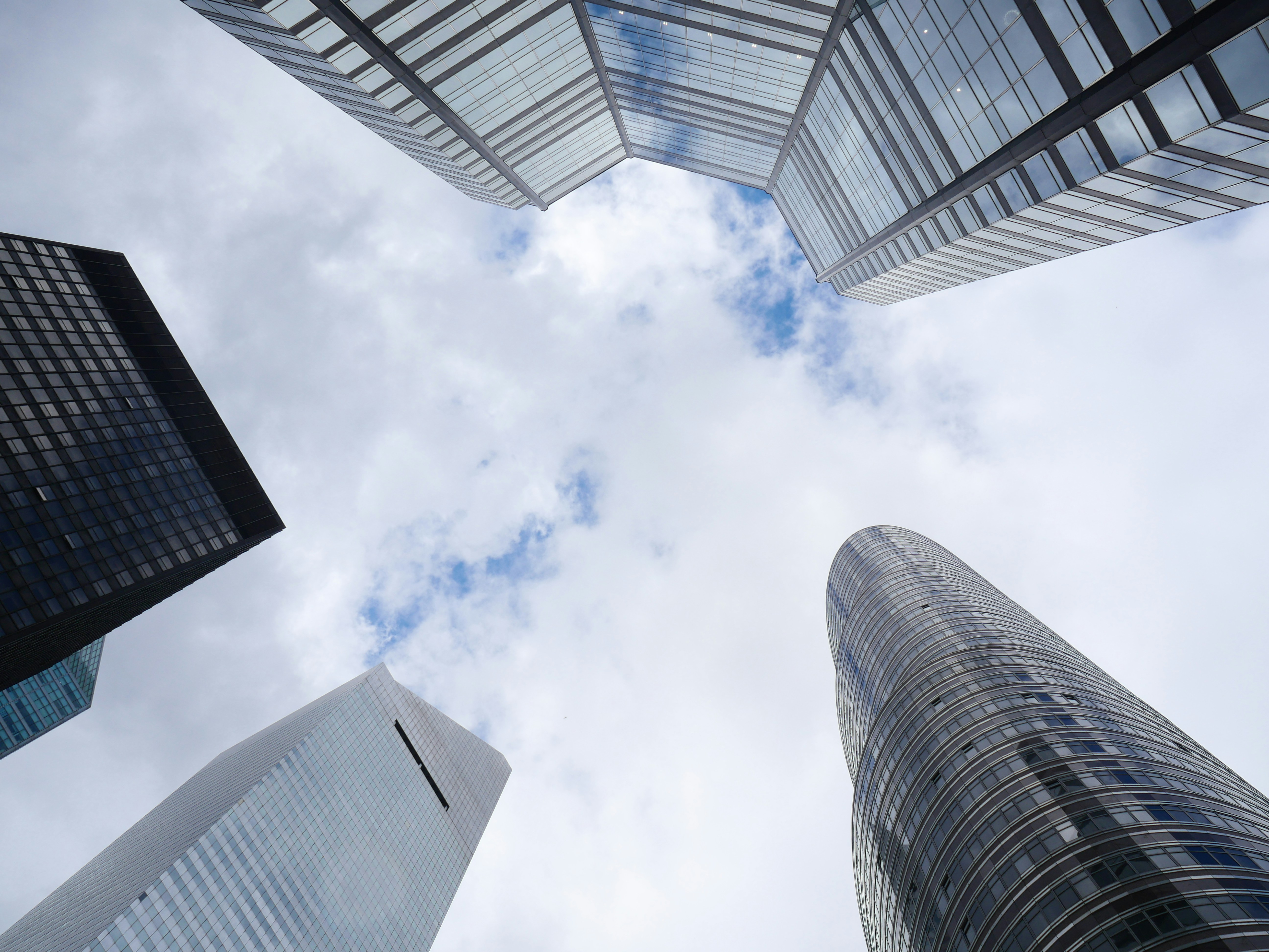 View from the ground looking up at towering skyscrapers with a cloudy sky above. The buildings create a dramatic vertical composition.