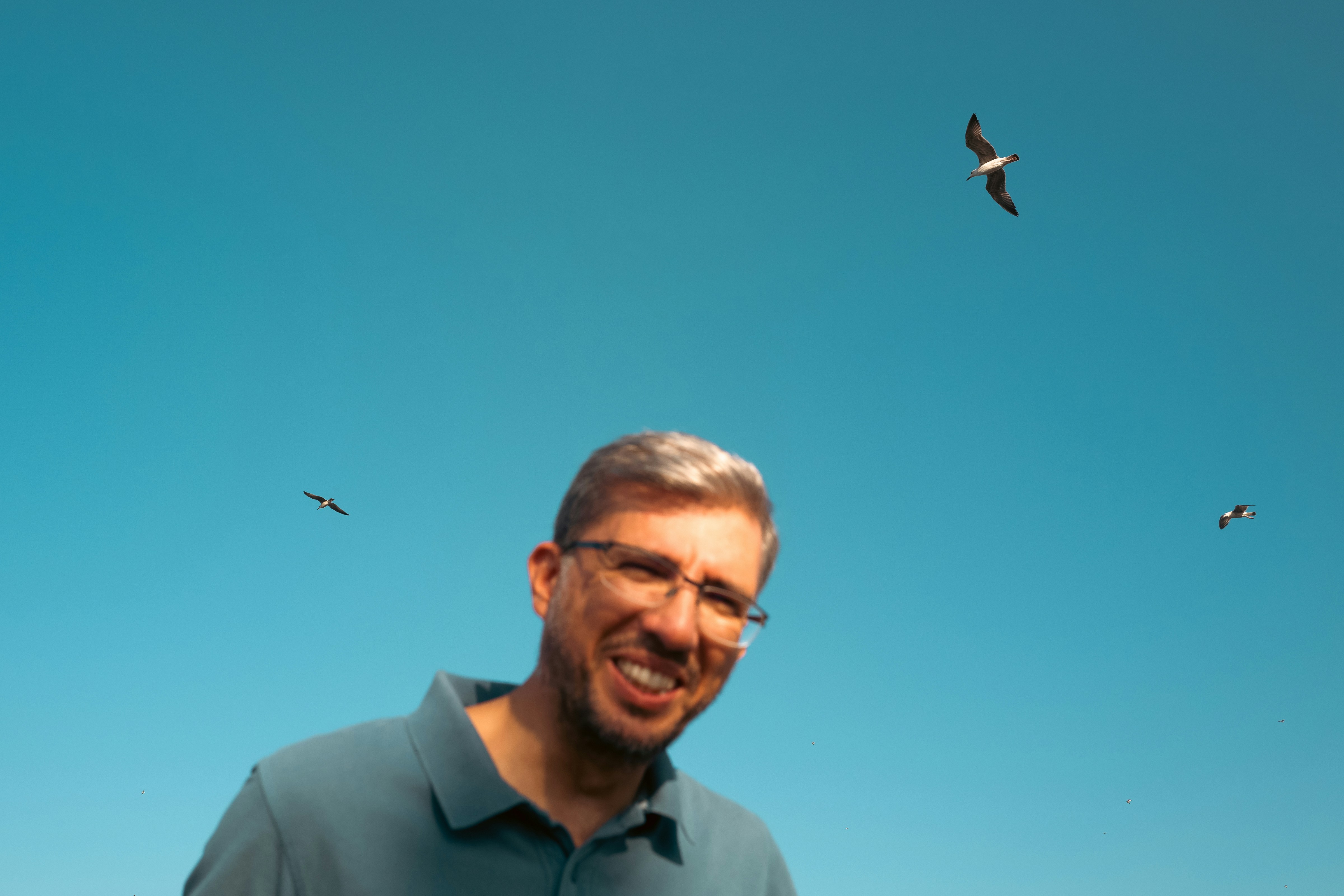 Man smiling with birds flying in clear blue sky