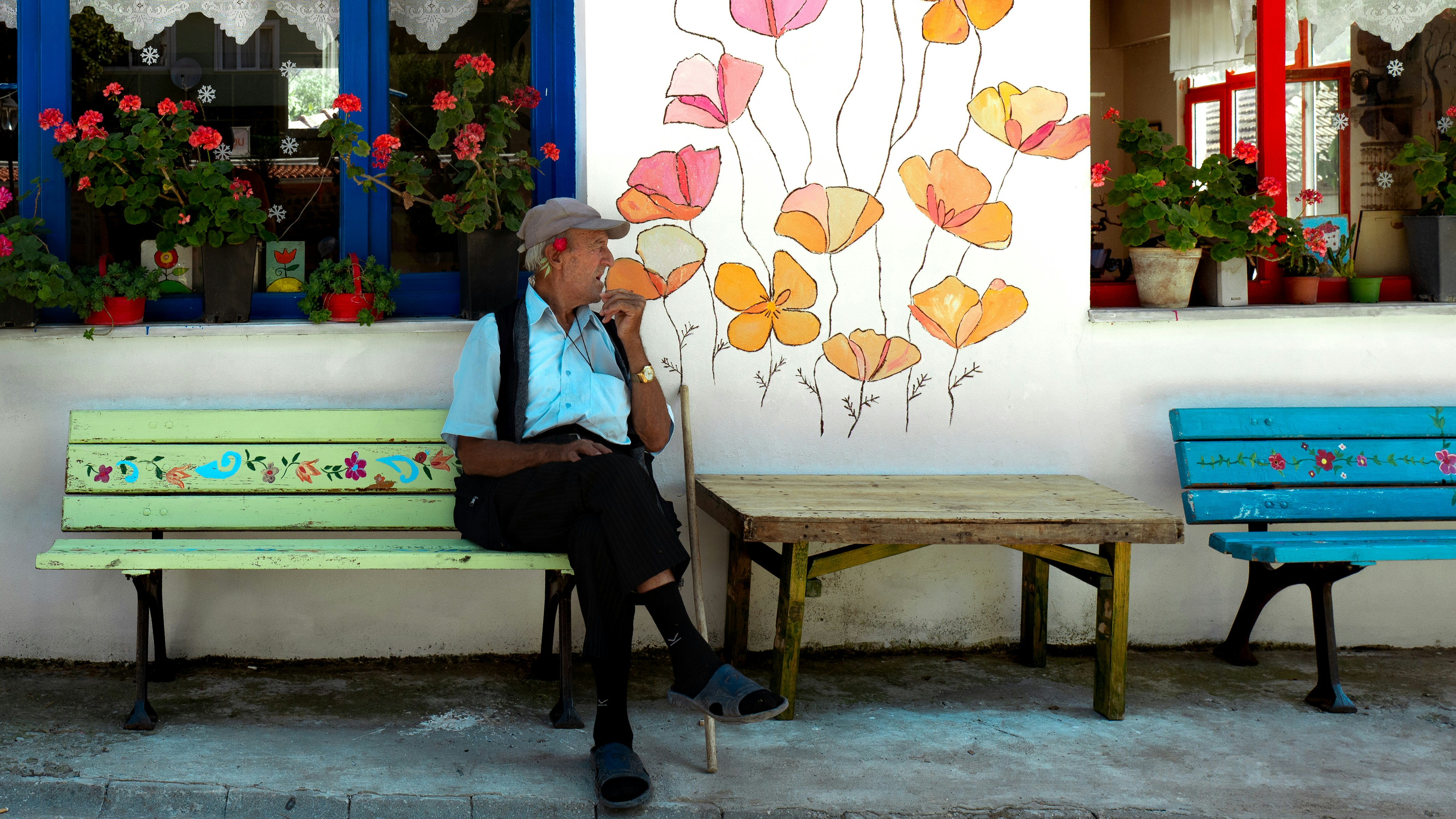 Man sitting on a bench by a wall with flowers.