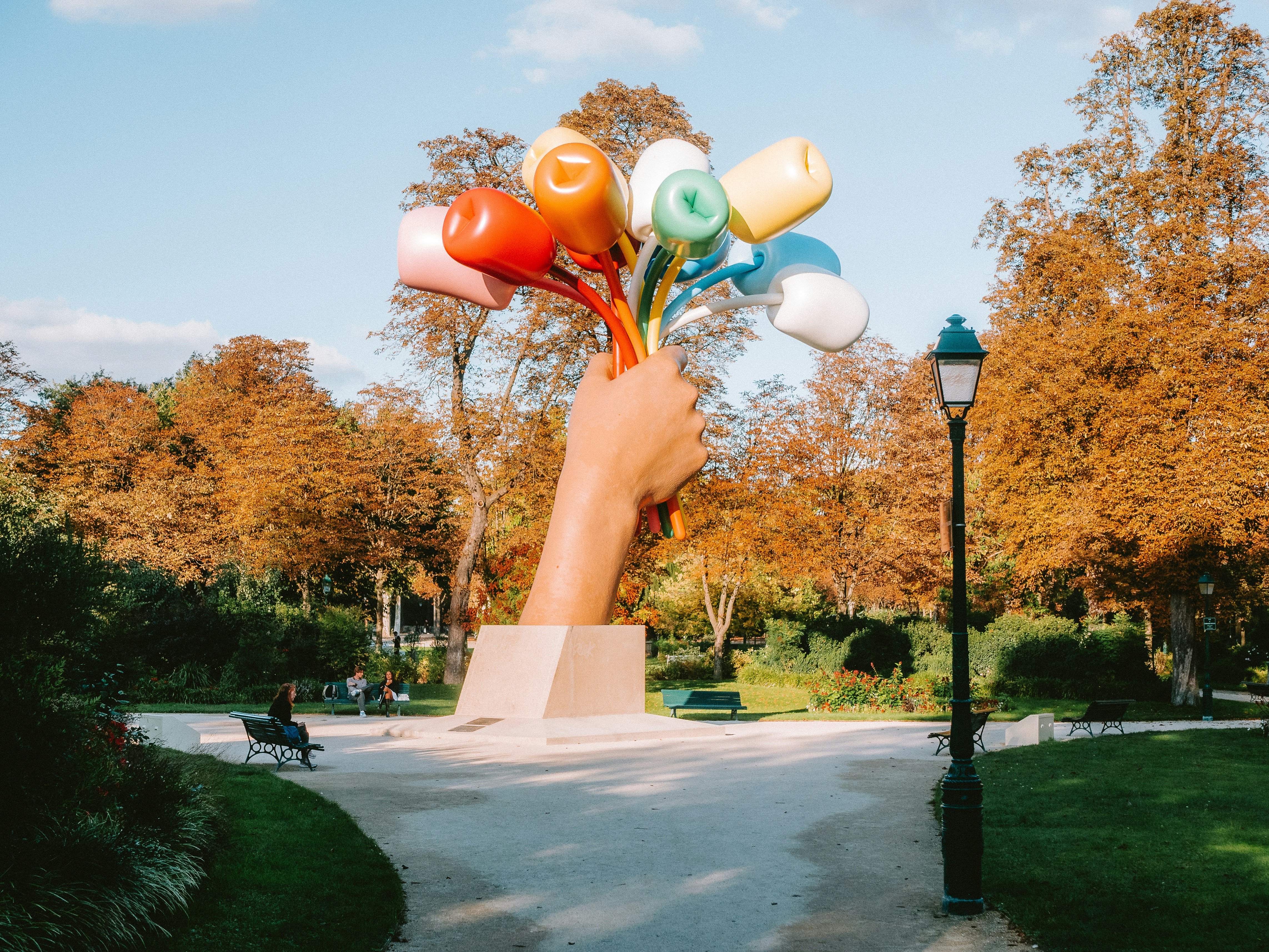 Hand and Helium: A Park Sculpture Embraces a Balloon Bouquet in Autumn Light