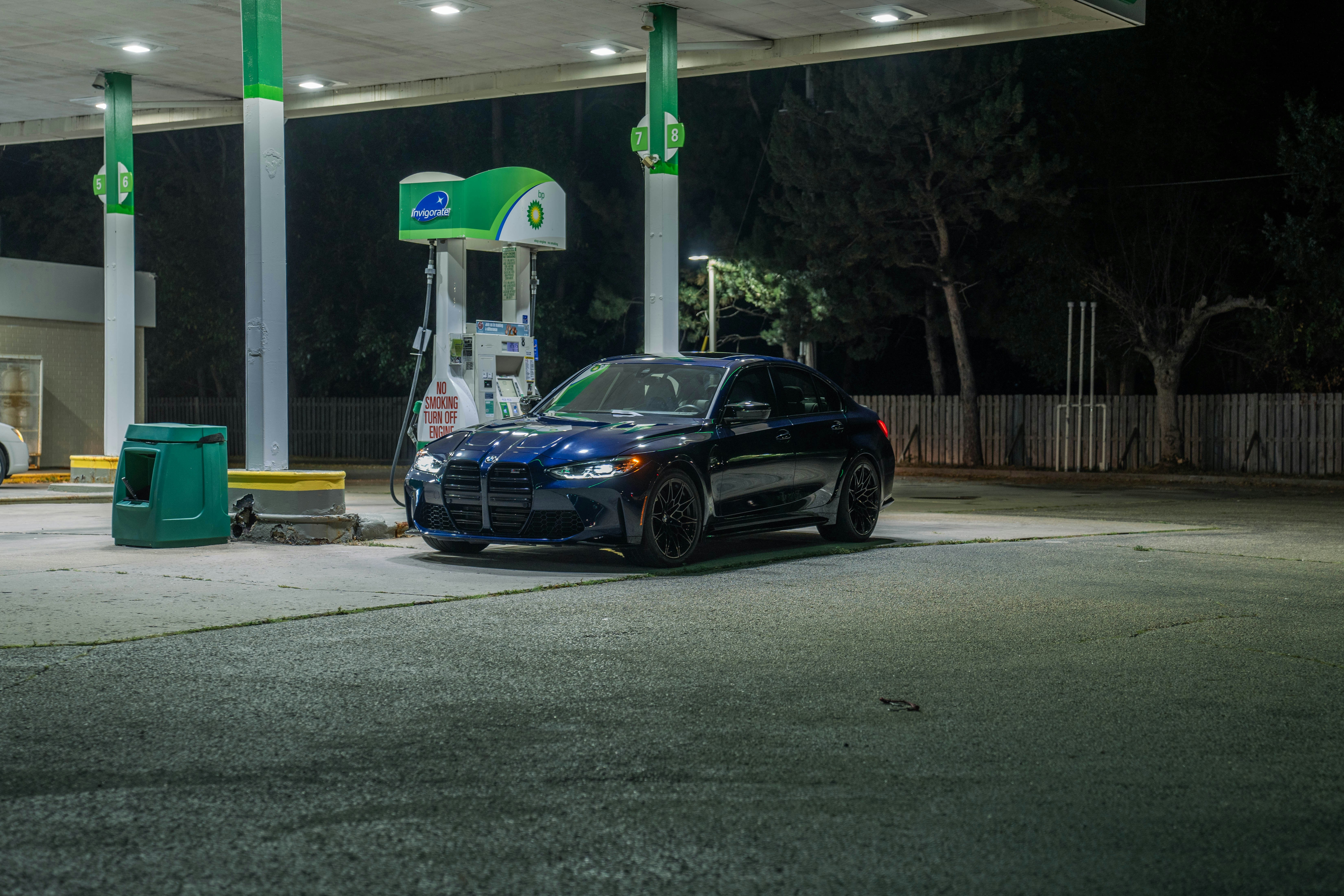 A sleek black sedan parked at a gas station under dim lights, showcasing its polished surface and modern design. The quiet night atmosphere enhances the car's presence.