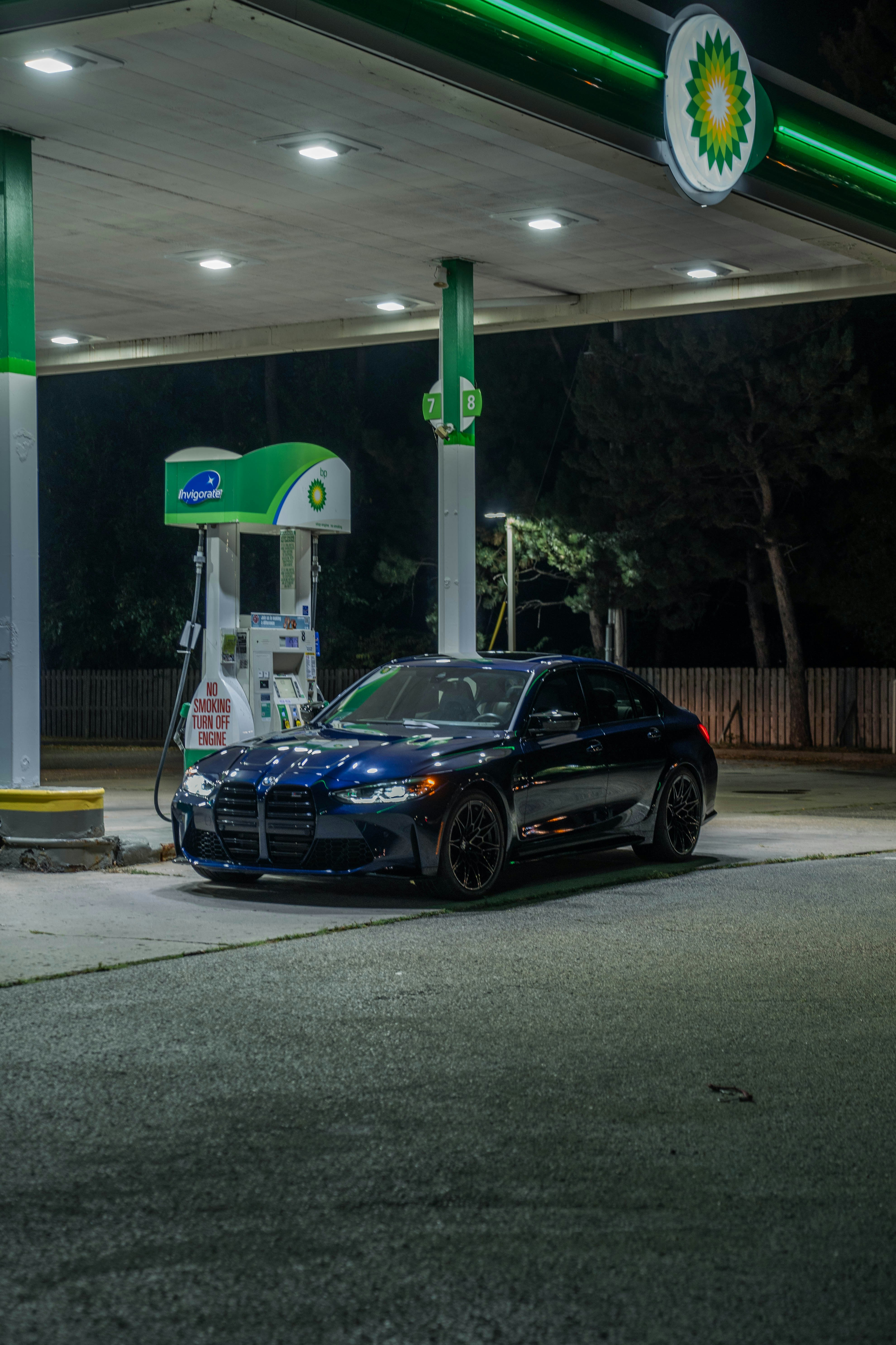 A sleek black car parked at a gas station under bright lights, showcasing its design against a dark backdrop. The station's branding is prominently visible.