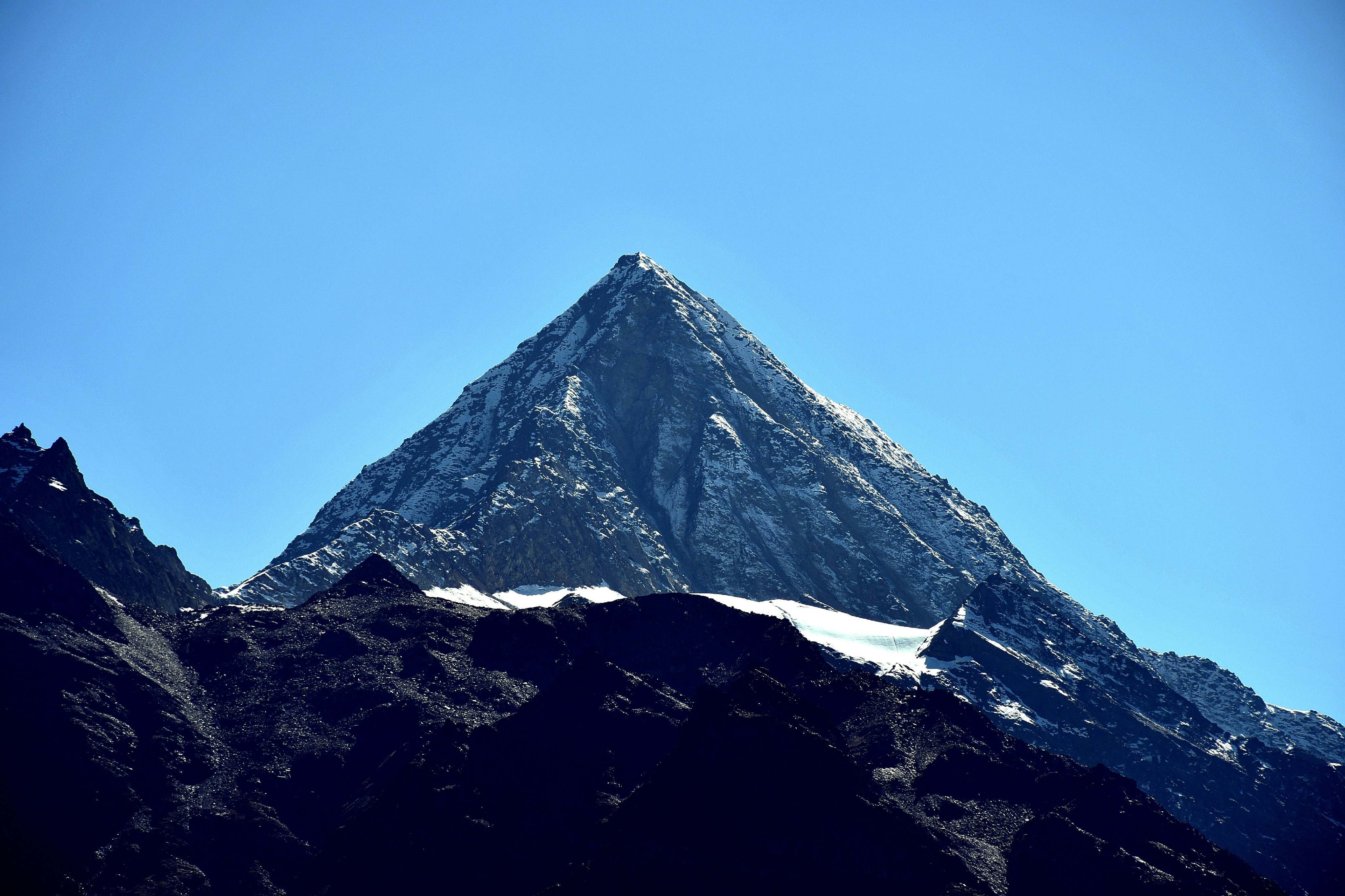 Snow-capped mountain peak rising sharply against a clear blue sky, showcasing the rugged beauty of nature.