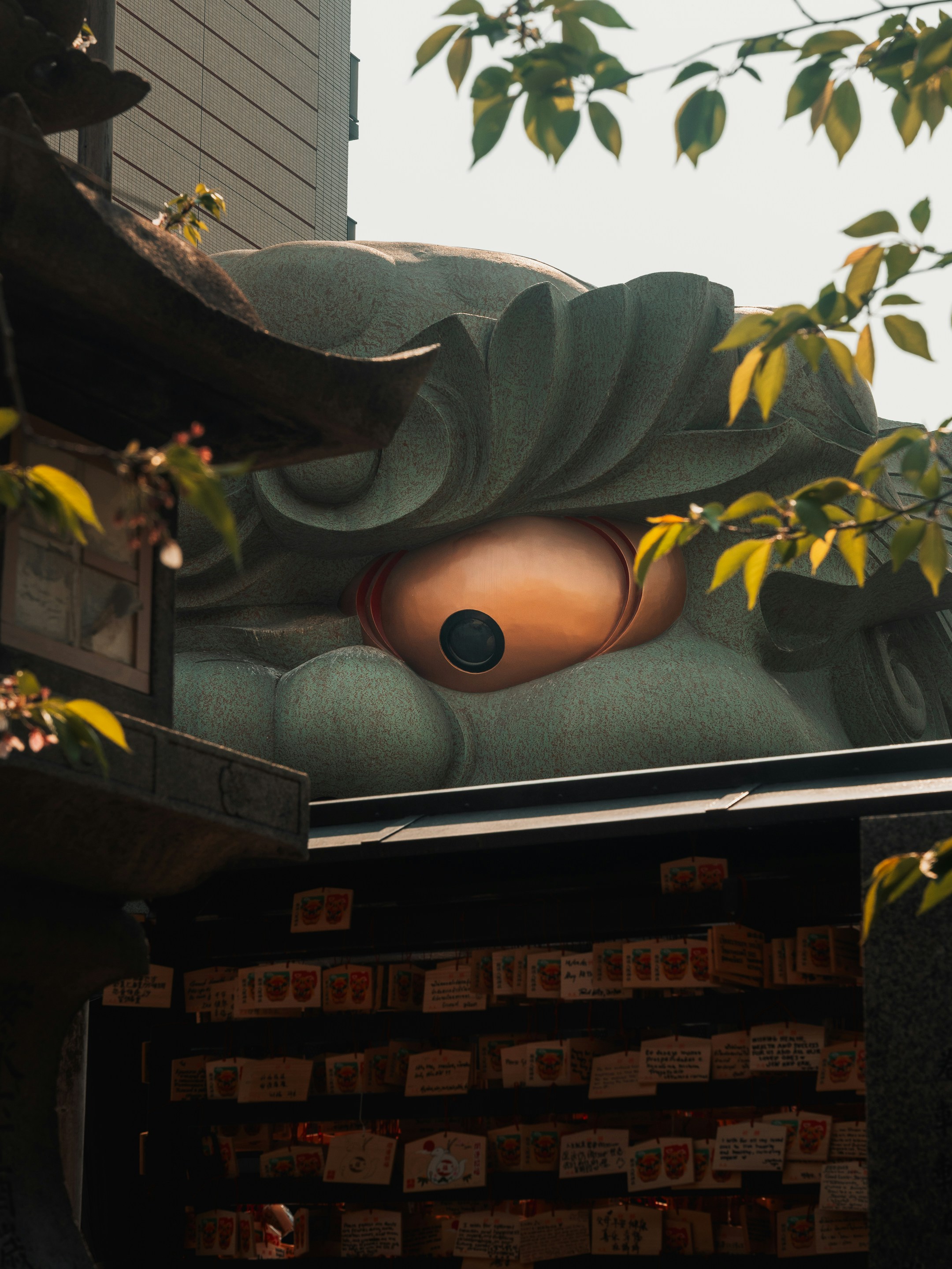 A large, intricately carved guardian figure peering through a traditional Japanese shrine, surrounded by vibrant foliage and offerings.