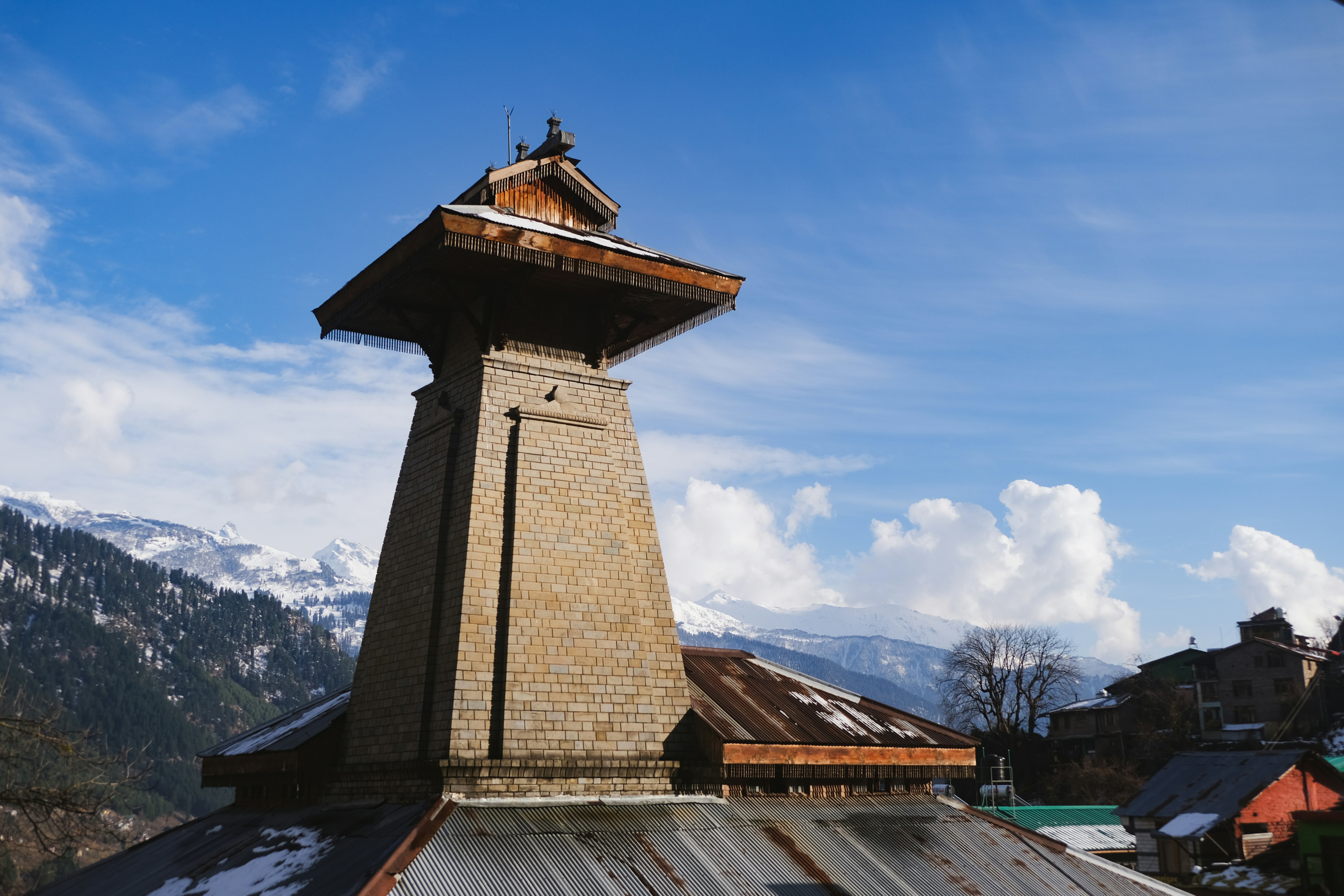 Historic wooden tower rising against a backdrop of snow-capped peaks under a clear blue sky.
