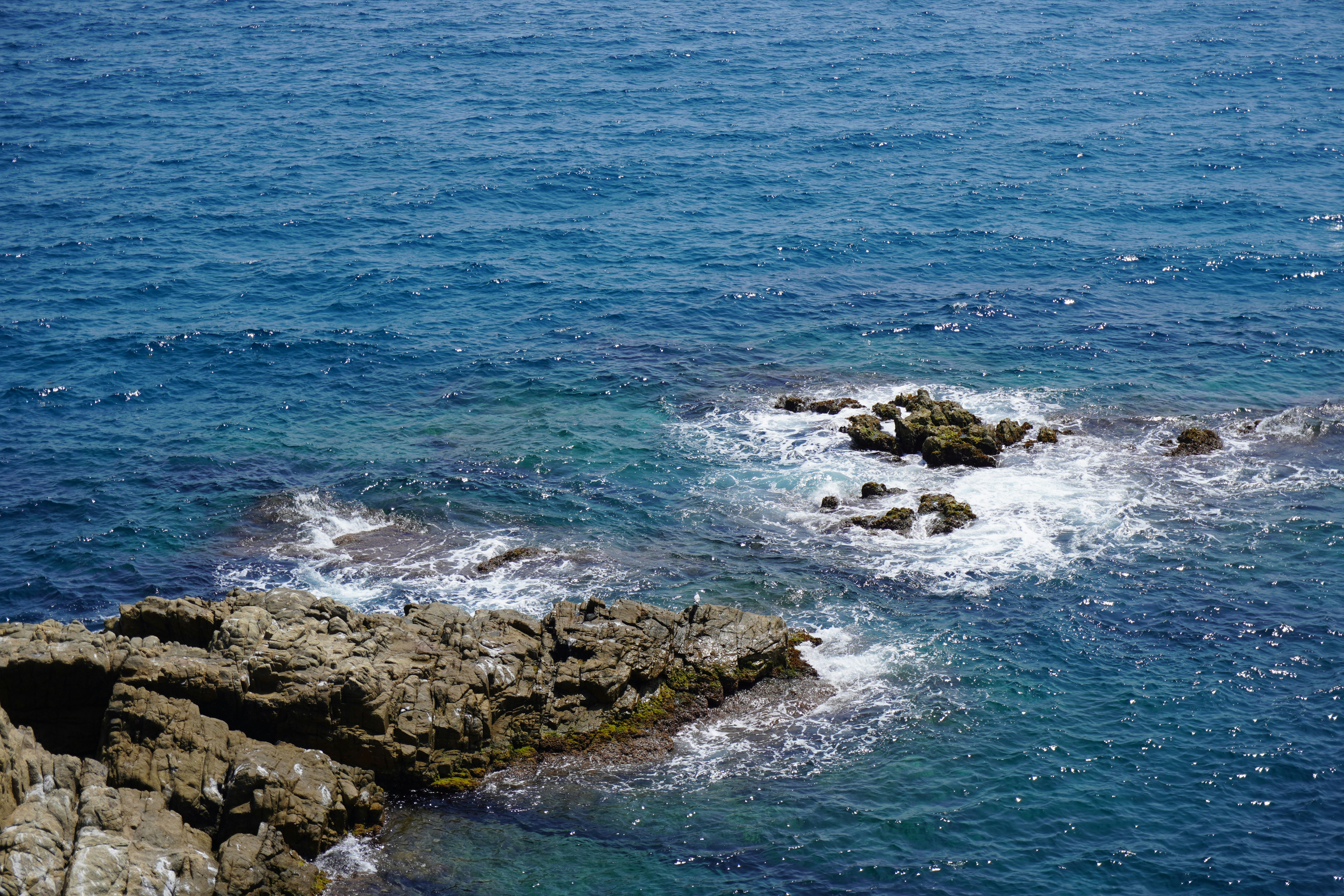 Waves crash against rocky shore on a sunny day.