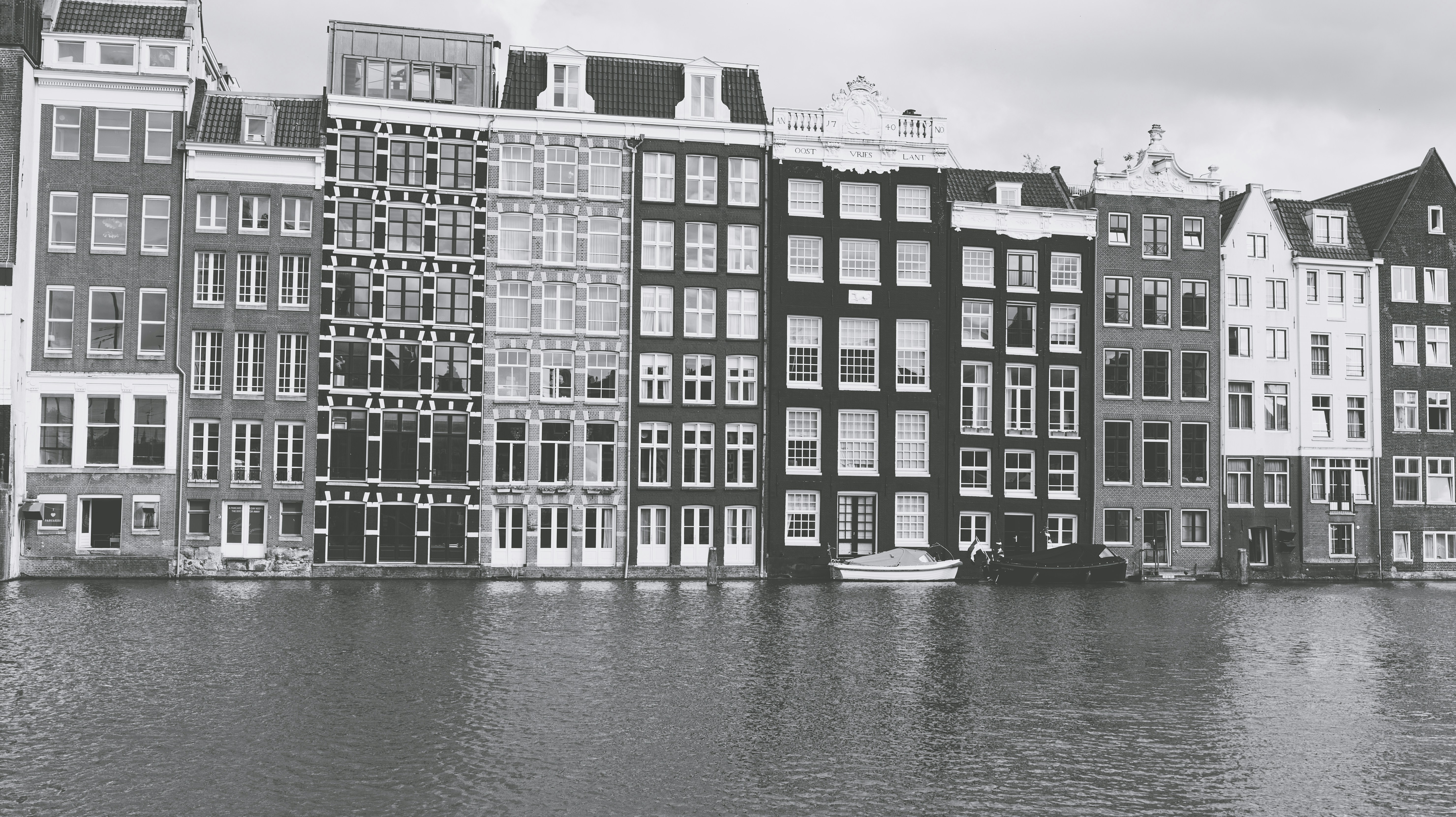 Row of historic canal houses in Amsterdam, captured in black and white, reflecting in the water below.