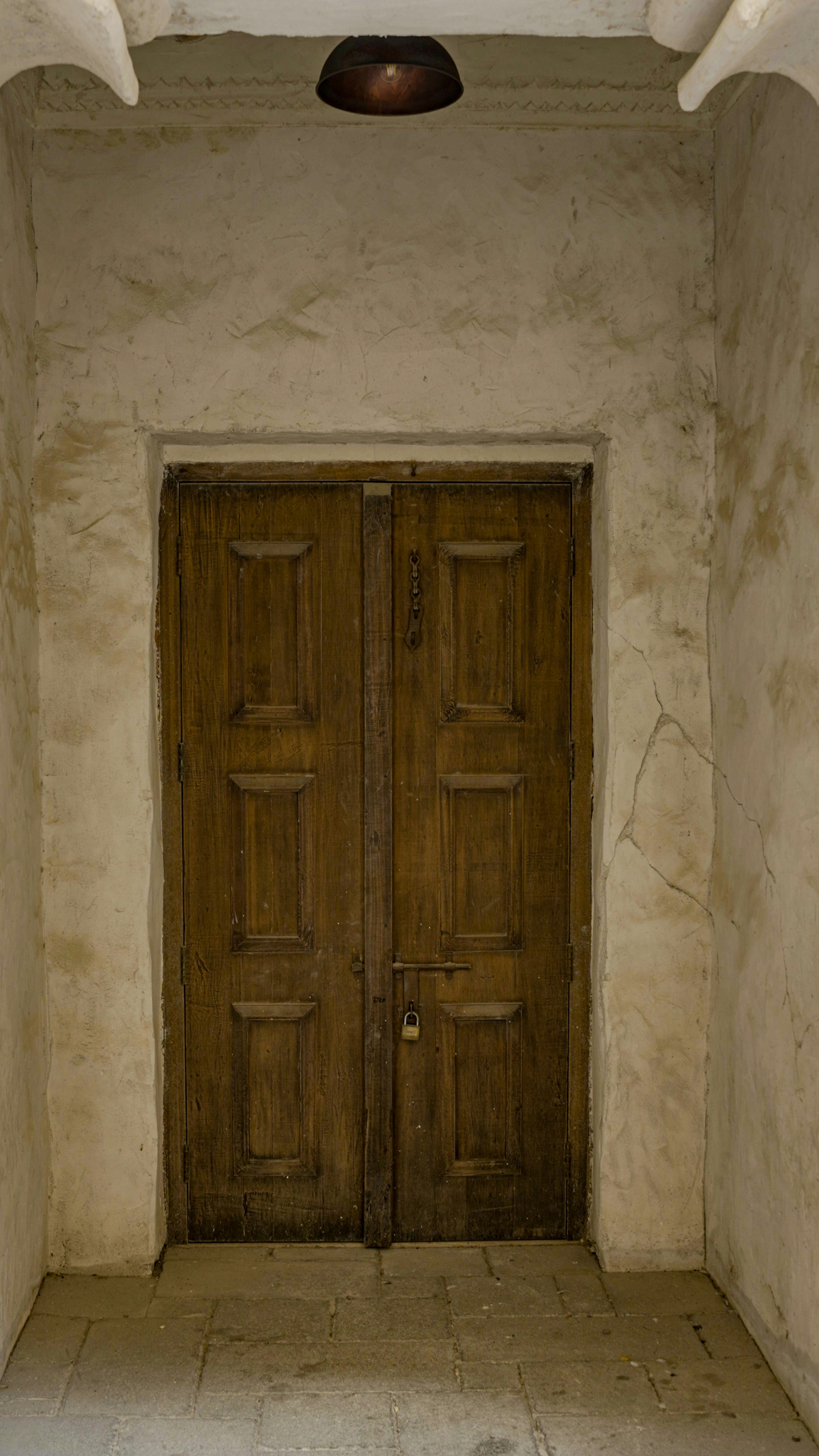 Weathered wooden double doors set in a textured, light-colored wall, hinting at stories behind the entrance.