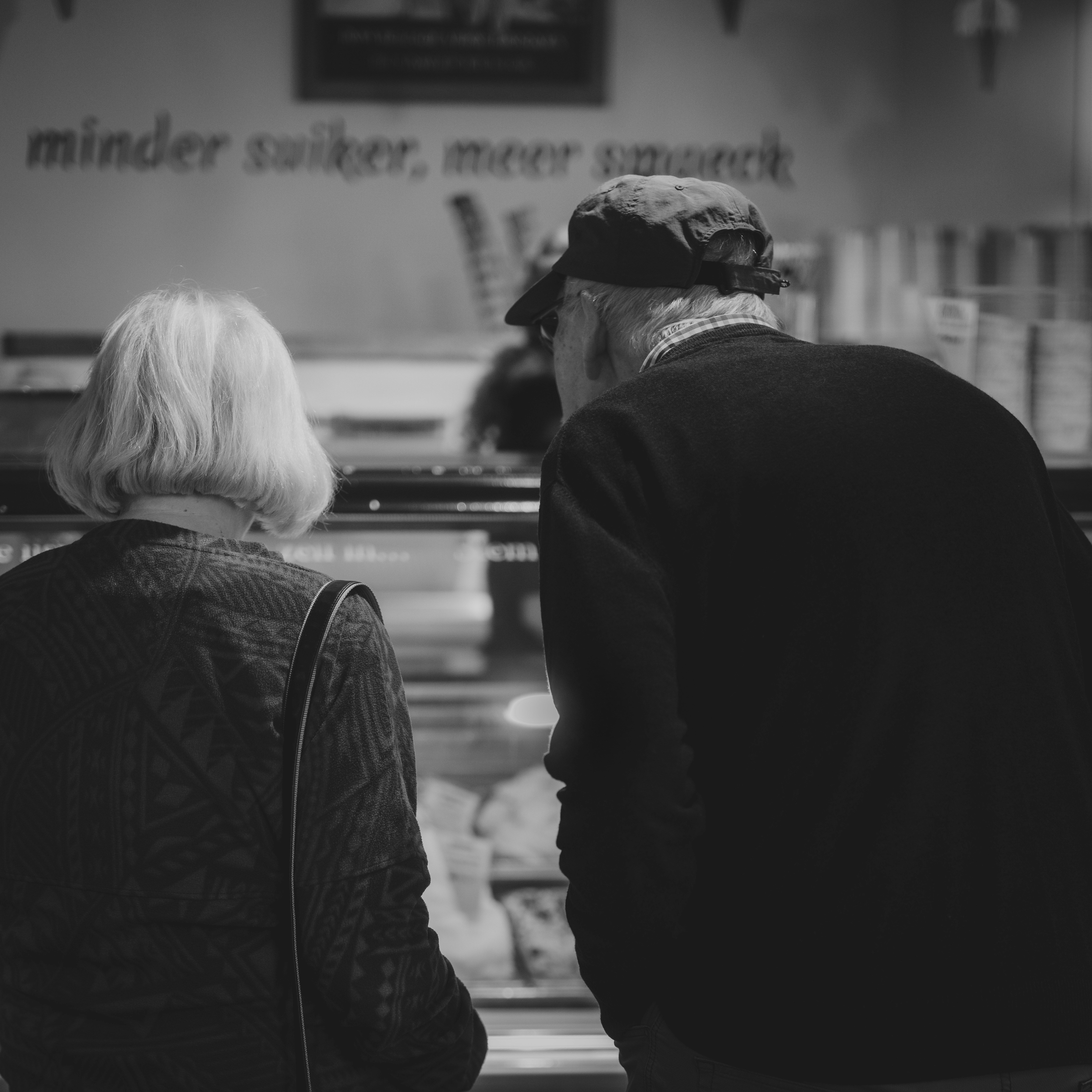 Two individuals observe a selection of treats in a cozy shop, their expressions reflecting contemplation and nostalgia.