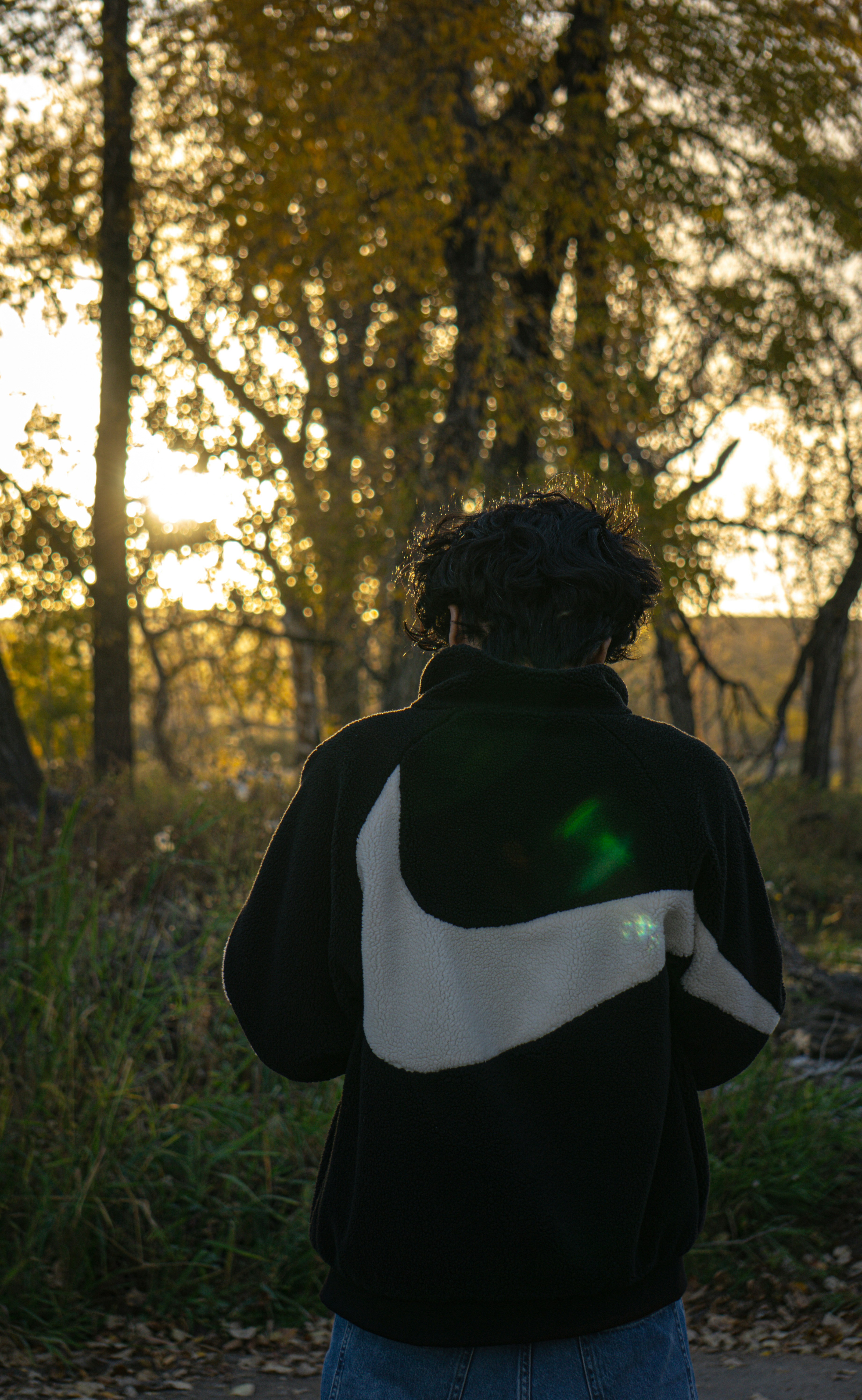 Person in fleece jacket facing trees at sunset