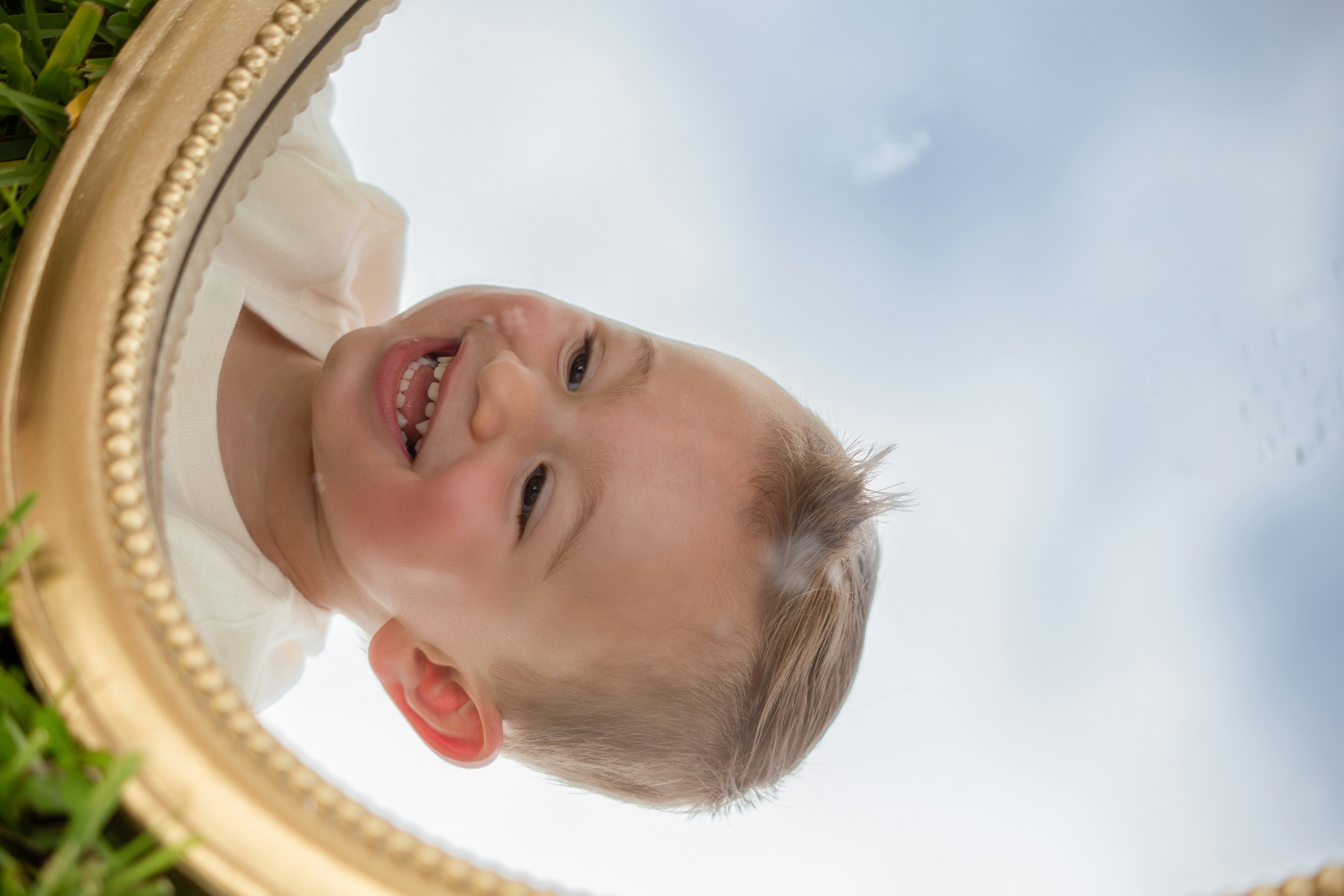 A smiling child reflected in a golden mirror.