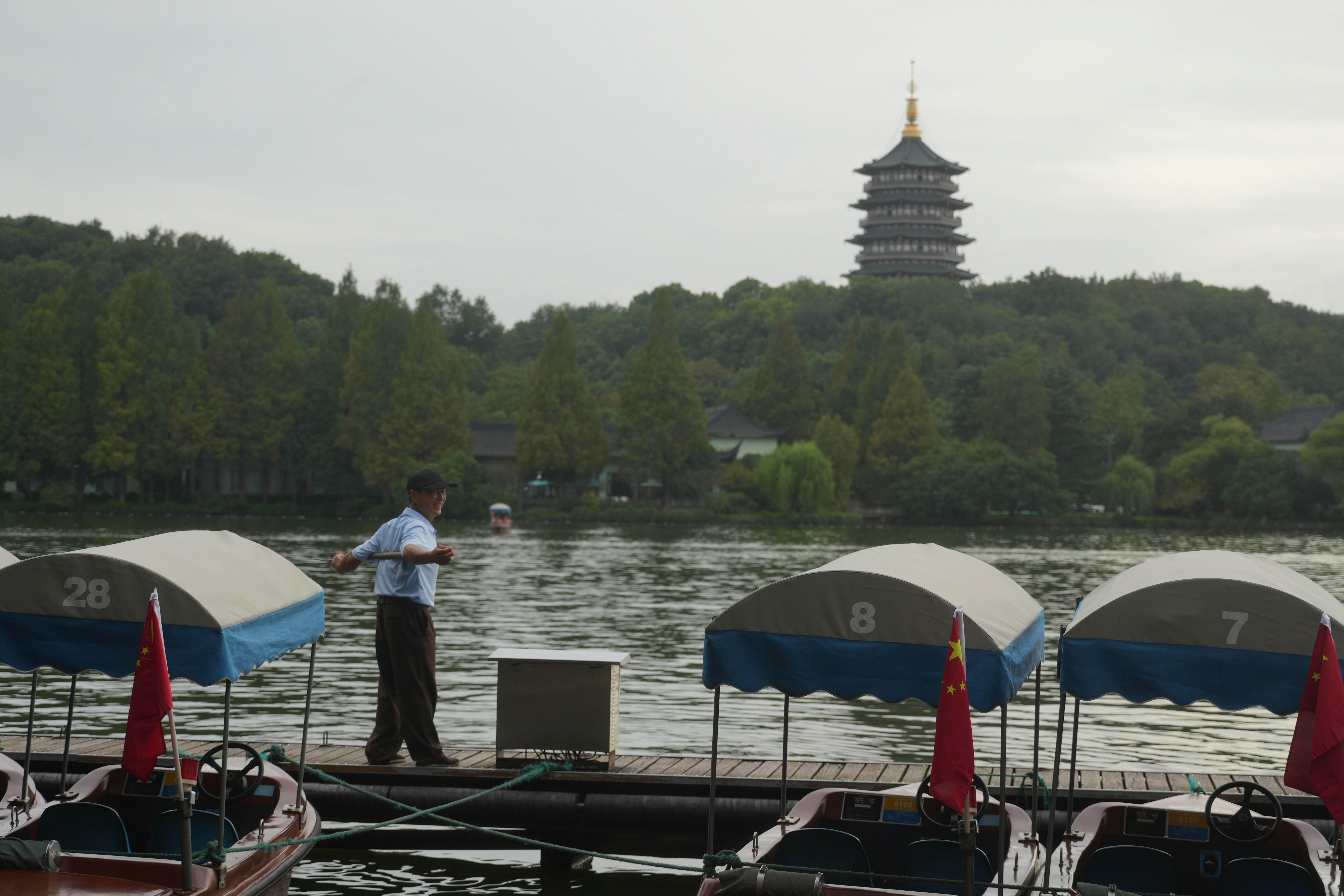 Man on dock with boats and pagoda in background.