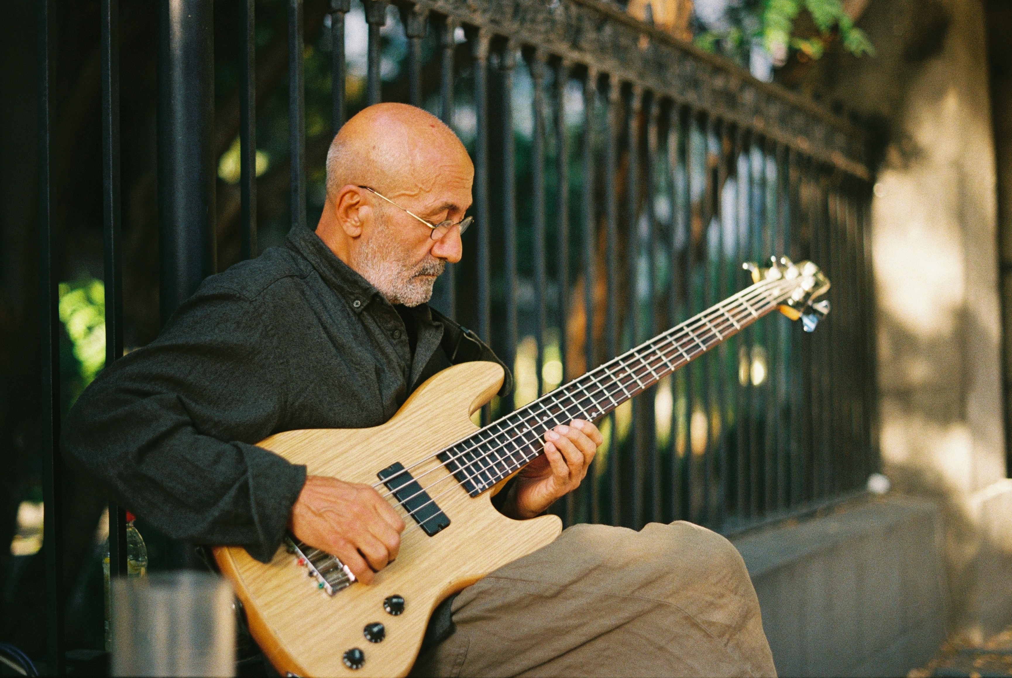 Musician skillfully playing a bass guitar on the street, surrounded by lush greenery and urban architecture.
