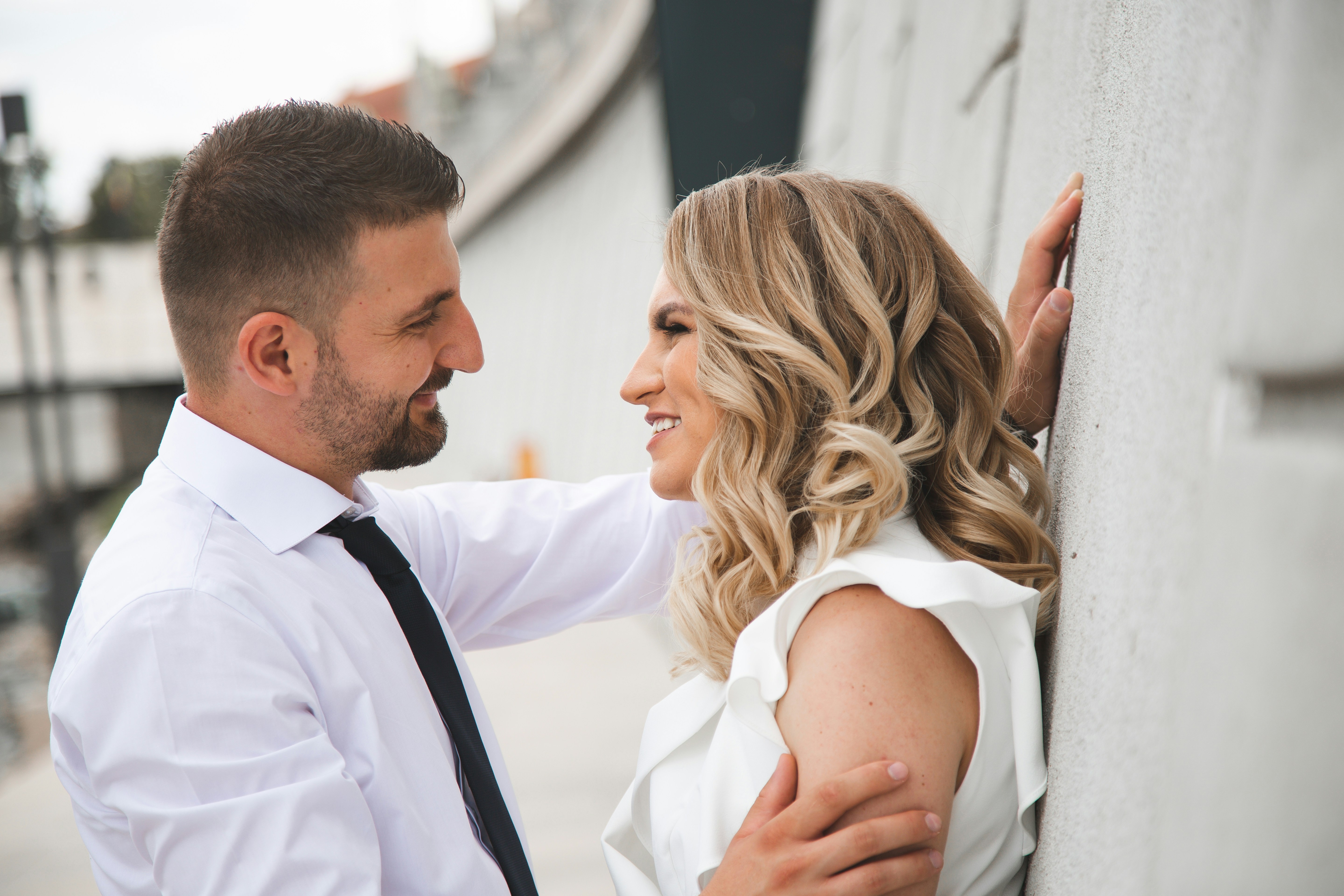 Man and his fiance close together, looking at each other and smiling. | A couple smiling at each other outdoors