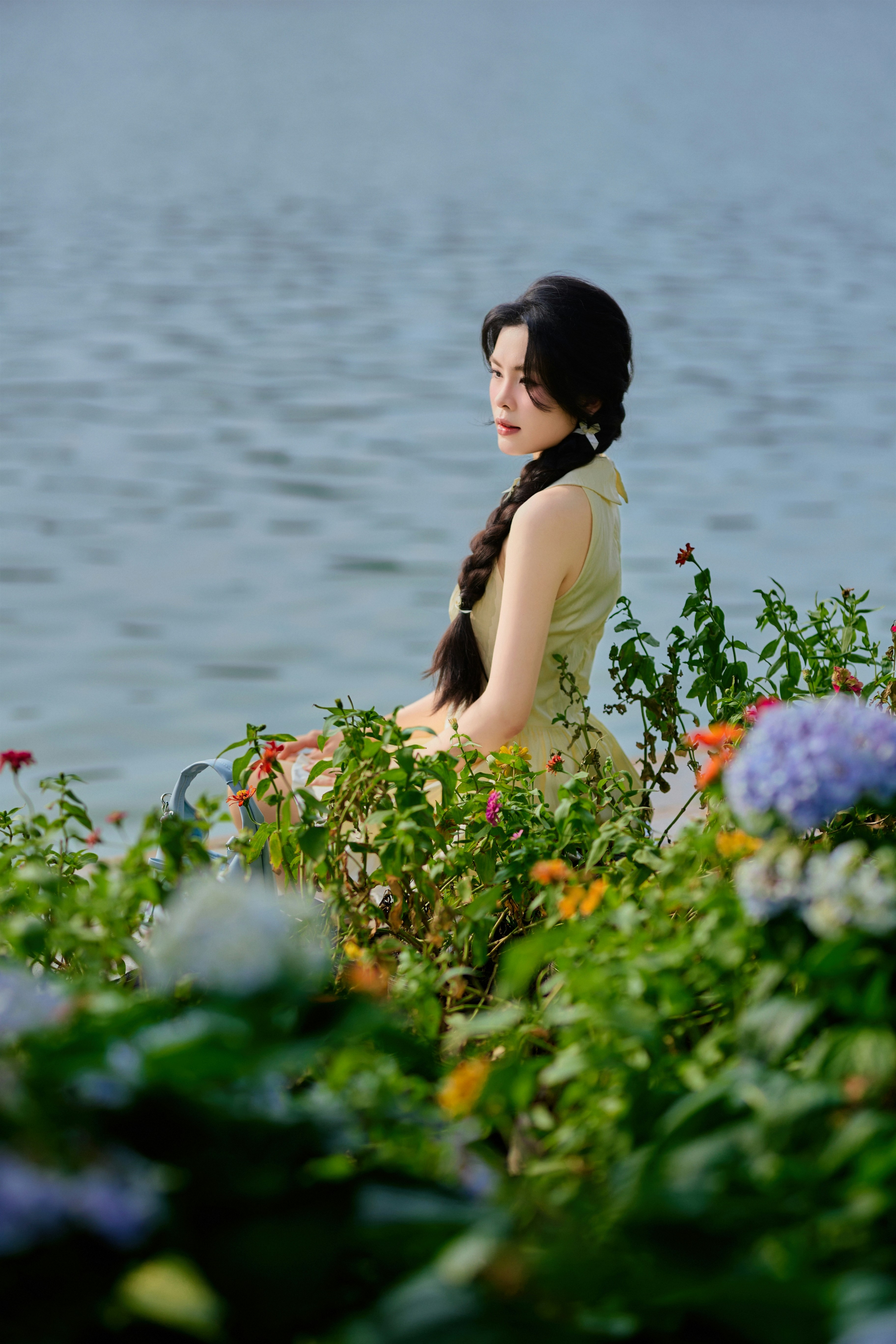 A beautiful young woman strolls through the autumn of Hanoi. | Woman in yellow dress by a lake with flowers
