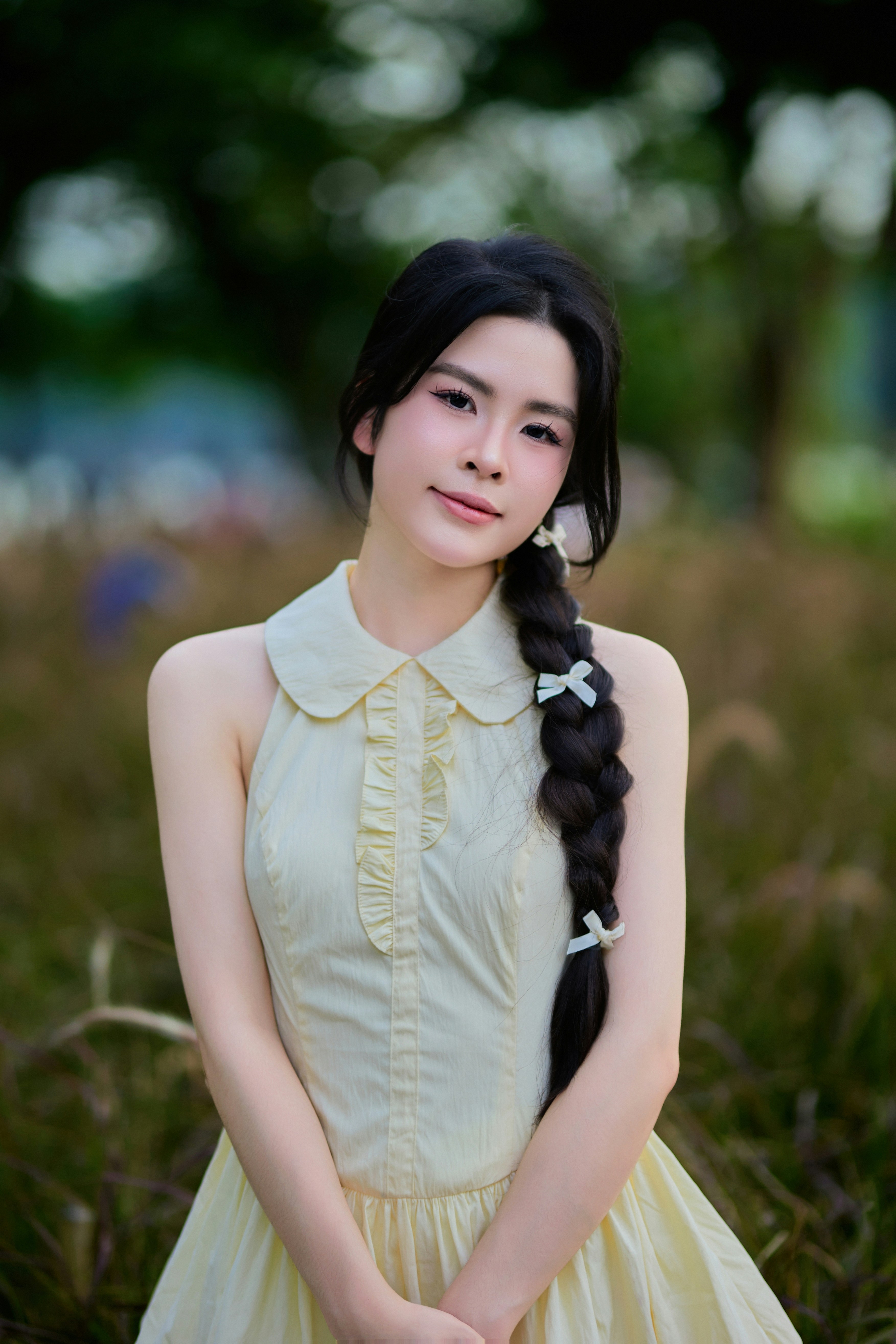A young woman in a soft yellow dress stands amidst lush greenery, her long braided hair adorned with white ribbons, exuding a serene charm.