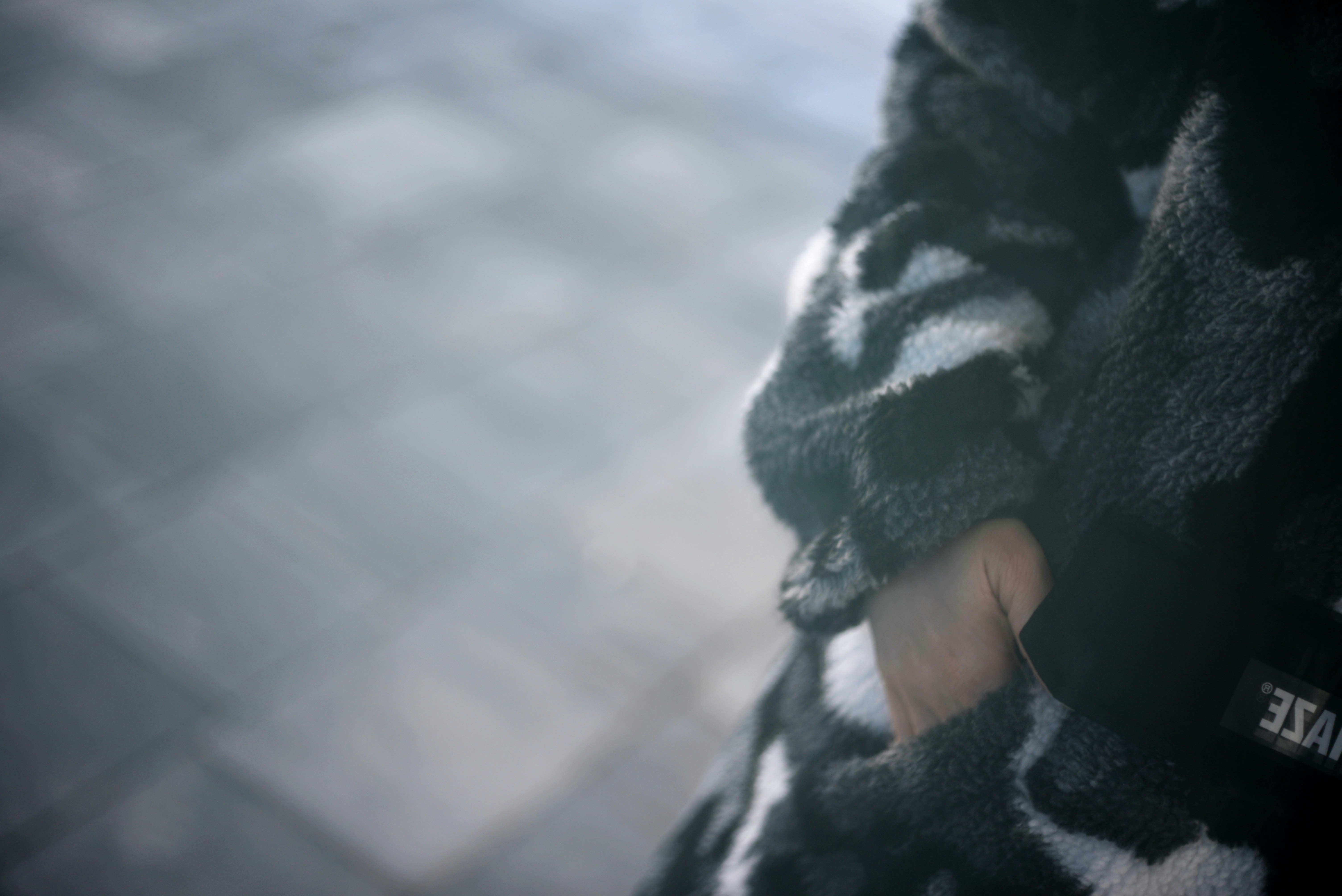 Close-up of a person’s hand tucked into a cozy, patterned coat, set against a blurred urban backdrop.