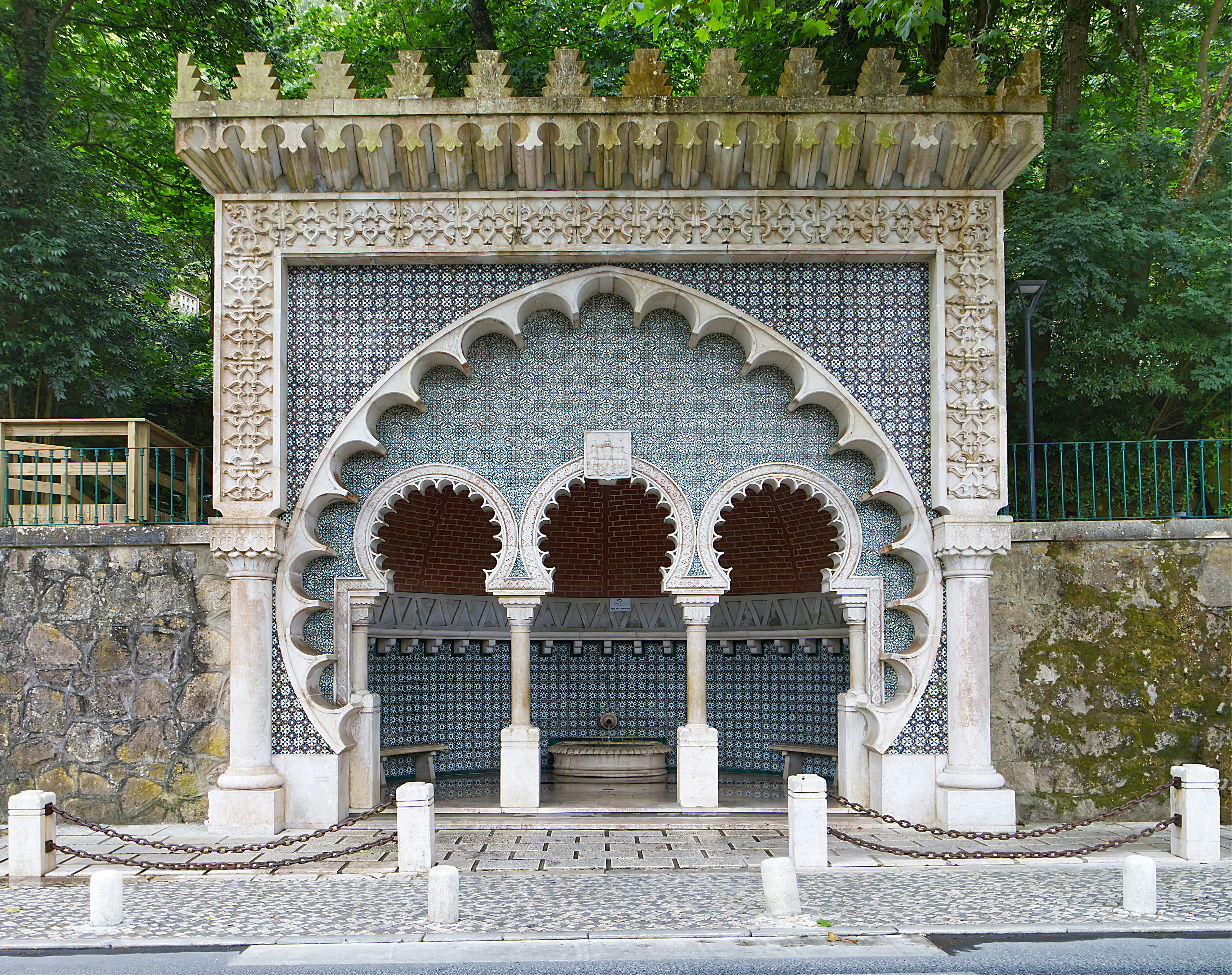 Nous continuons notre ascension pédestre vers le célèbre palais de Sintra en empruntant la Volta do Duche, à deux pas du centre historique de Sintra, nous croisons la Fonte Mourisca. Cette fontaine est l’œuvre du maître José da Fonseca. Elle a été démontée en 1960 pour permettre l’élargissement de la route, et a été patiemment reconstruite vingt ans plus tard. | Ornate tiled fountain with arched openings and columned alcoves.