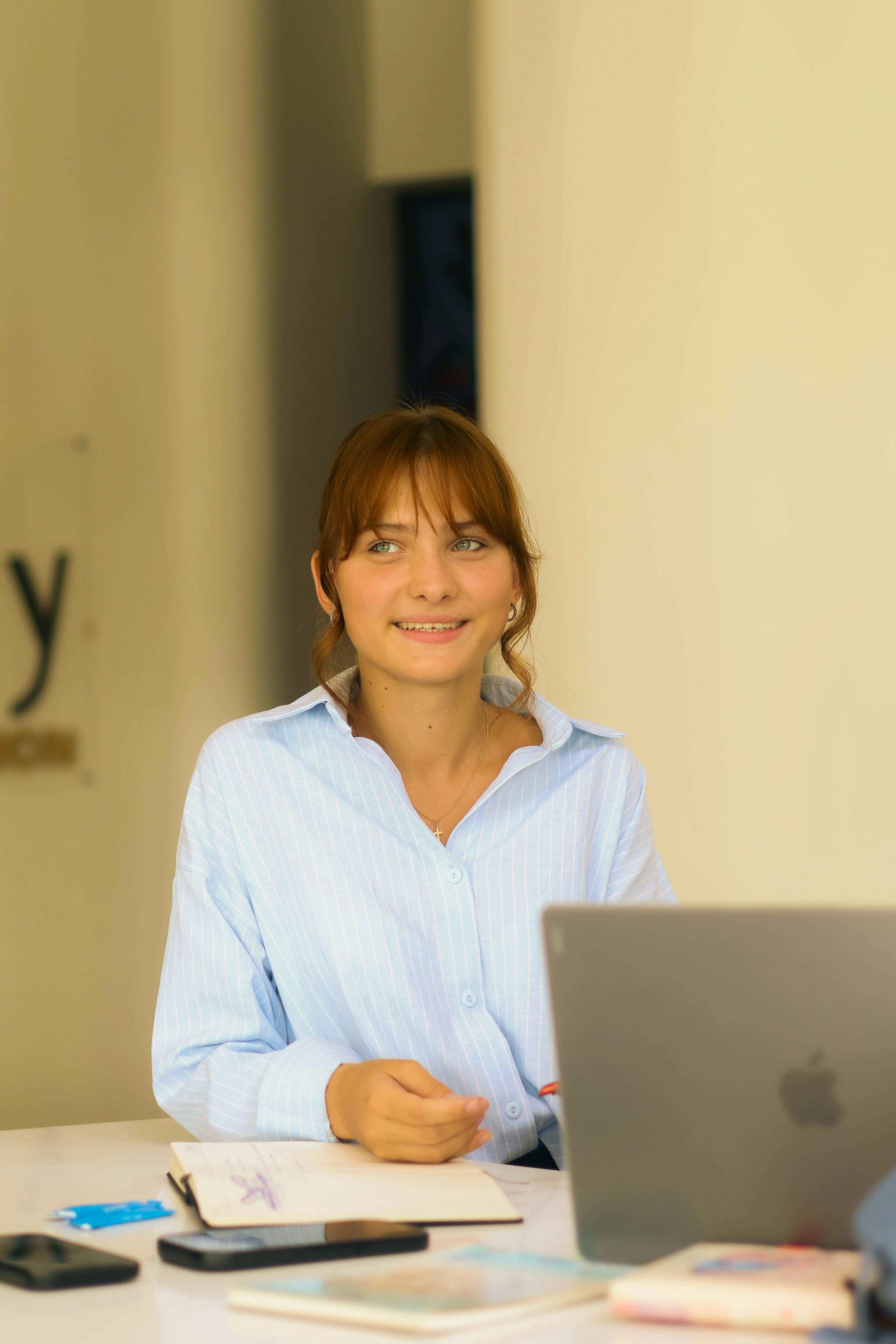 A girl smiling | Young woman in light blue shirt at desk with laptop.