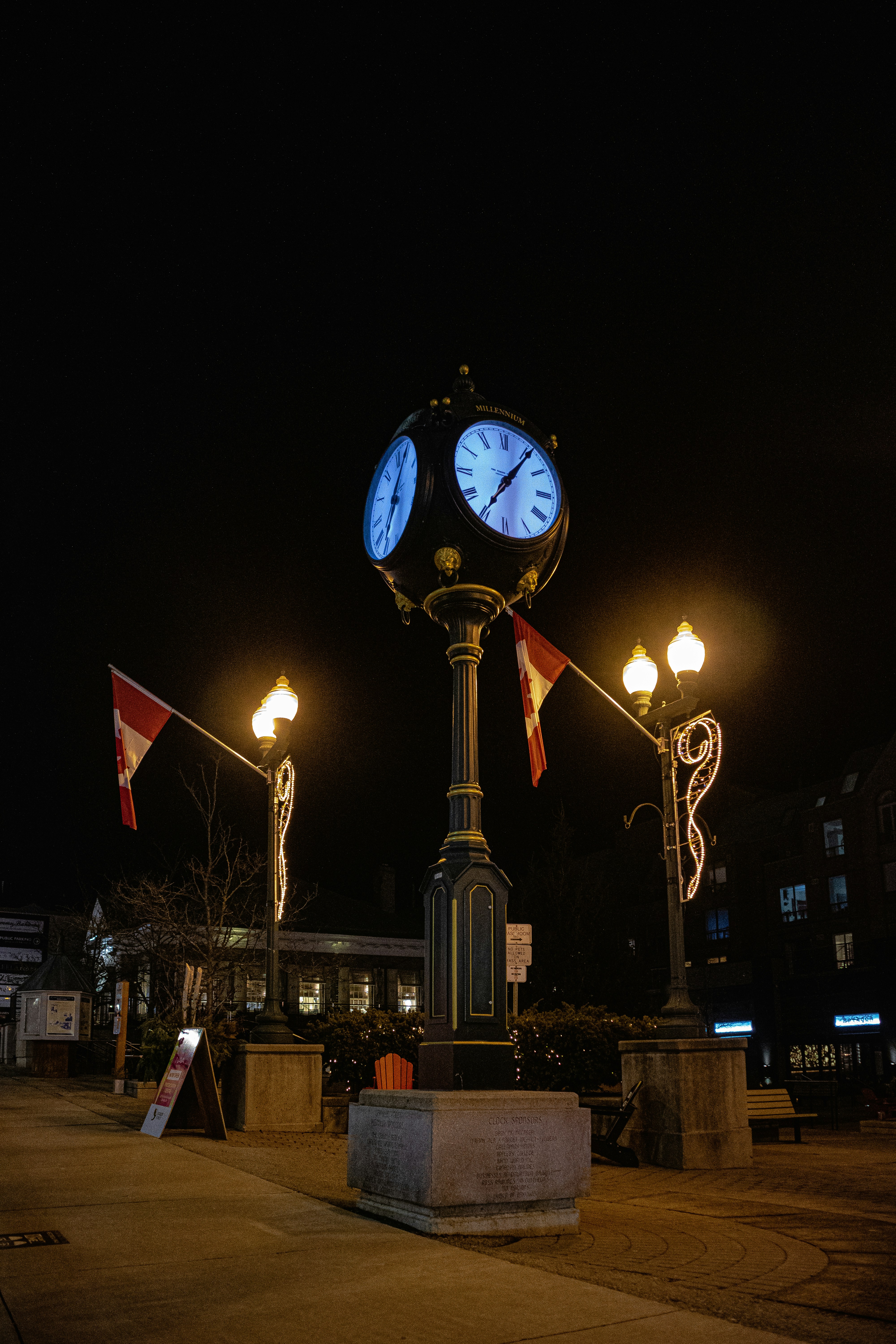 A vintage clock tower with canadian flags at night.
