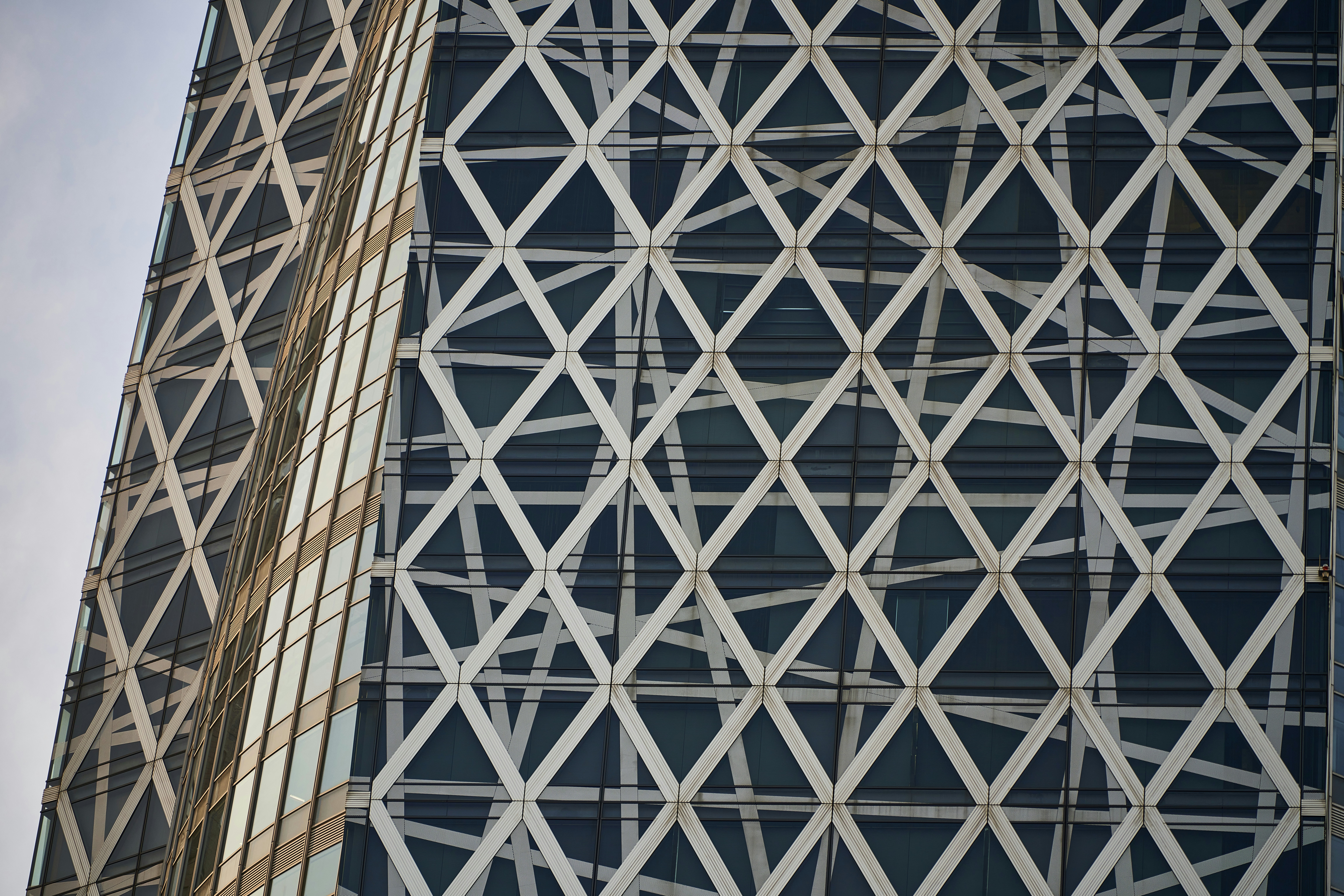 A huge construction crane rests against the glass wall of a modern skyscraper nearing completion. The cool, geometrically patterned façade of the building contrasts sharply with the crane's rugged steel frame, painted a vibrant red. This is the dynamic moment when a city is growing and the landscape of the future is taking shape. This photograph is filled with the creative and developmental energy inherent in the act of construction. | Modern skyscraper with geometric patterned facade