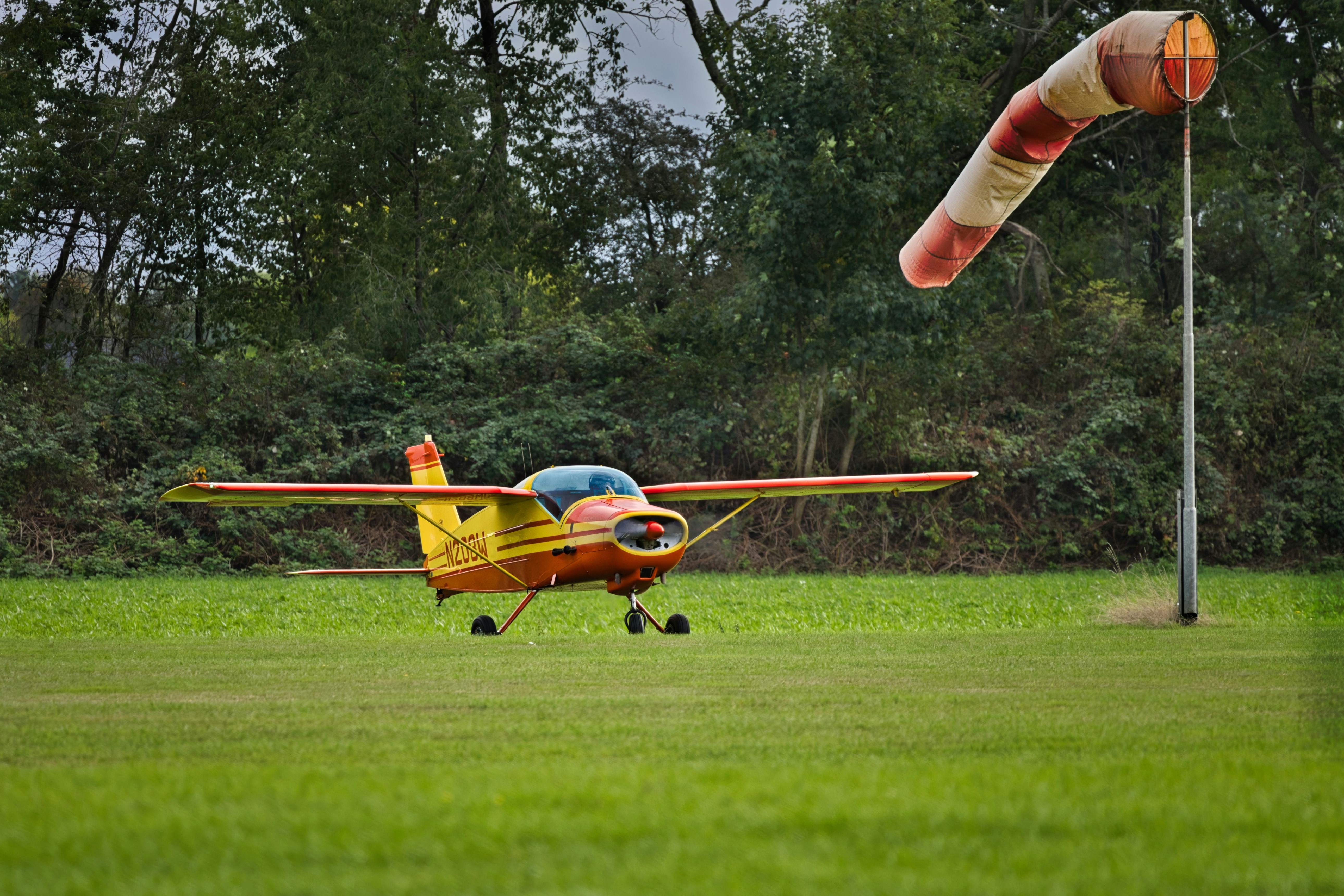 Yellow Sport Plane Resting at a Quiet Grass Airfield by the Striped Windsock