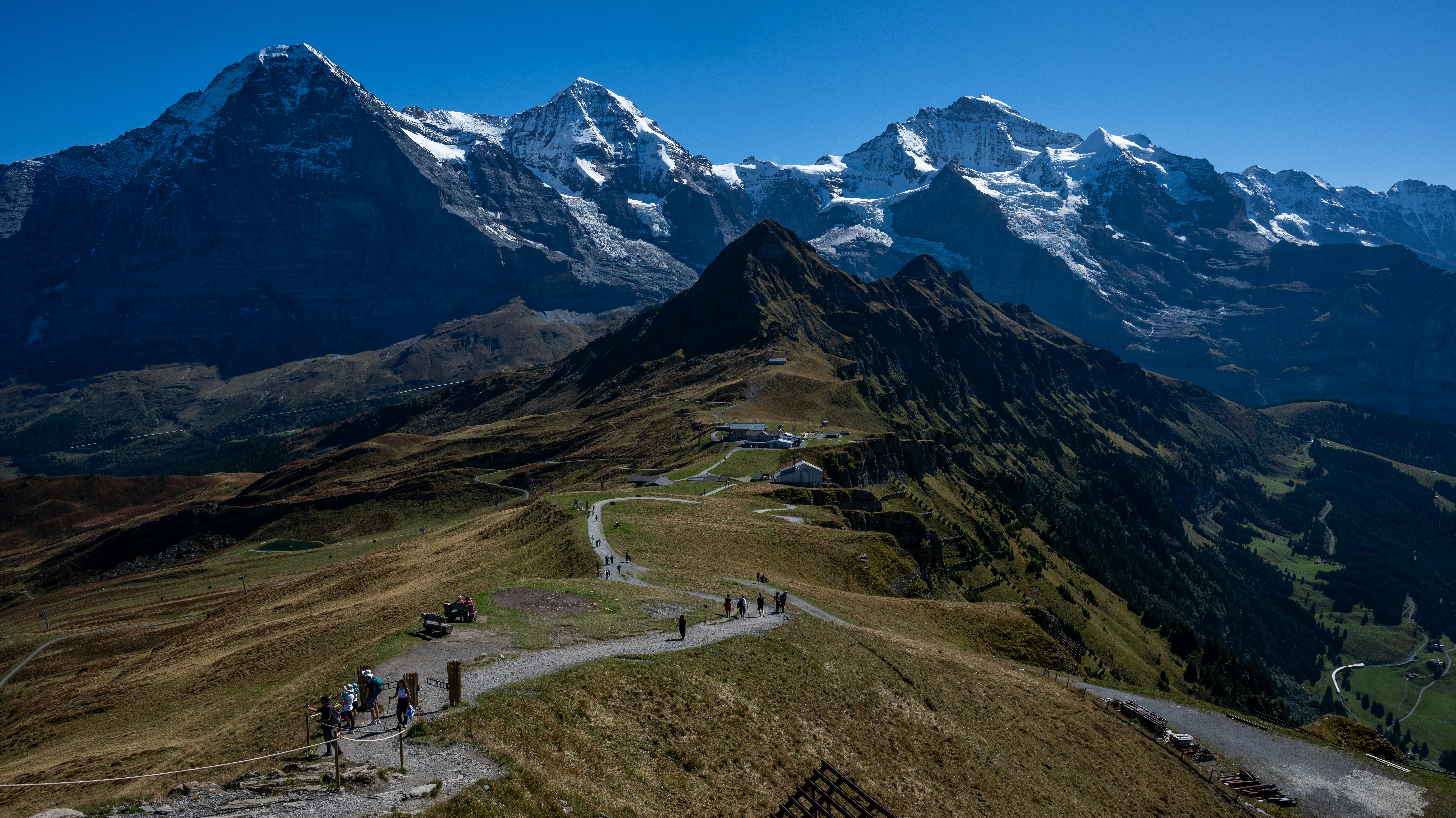 Hikers on a mountain trail with snowy peaks behind
