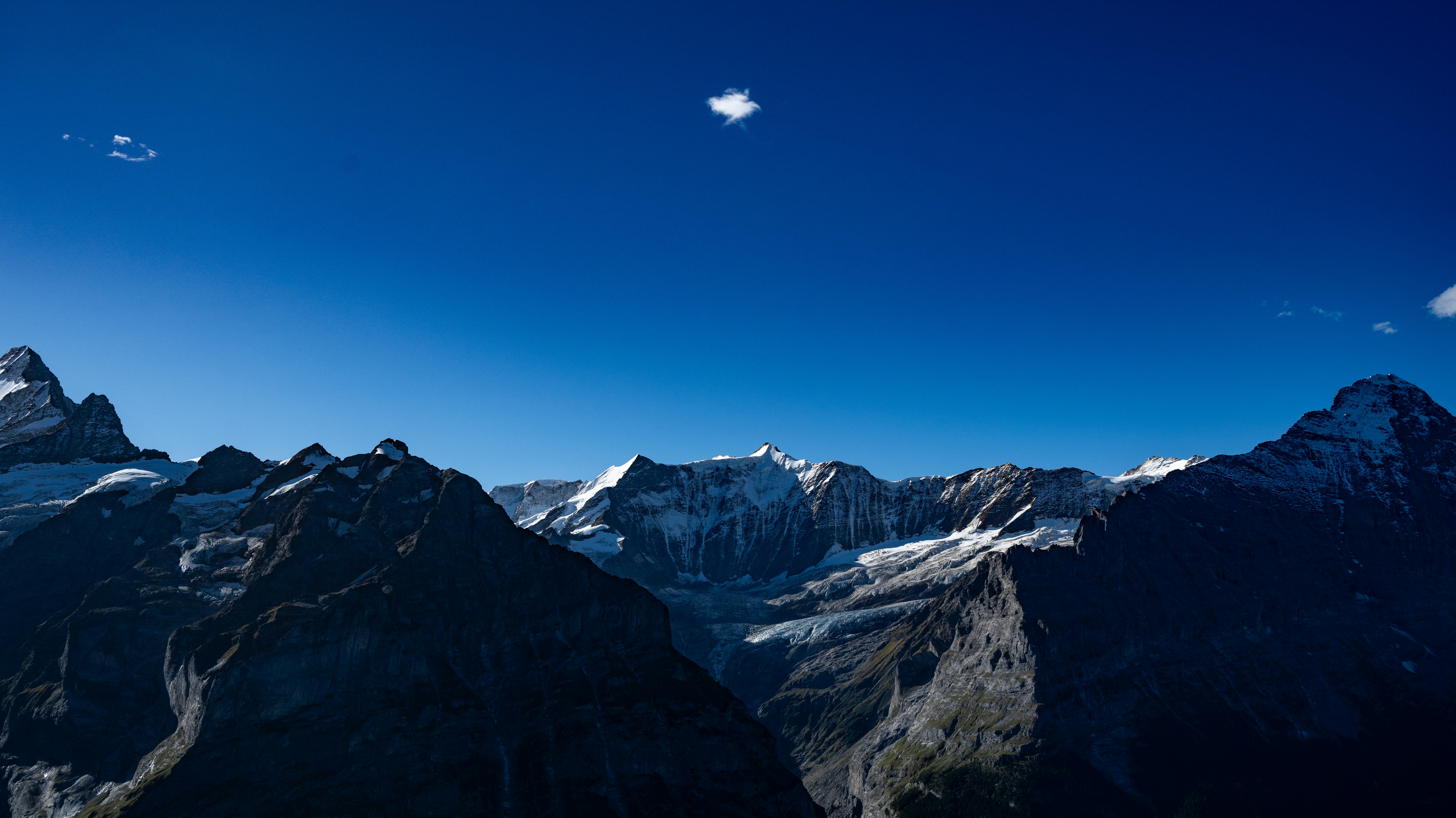 Majestic mountain range under a clear blue sky, showcasing snow-capped peaks and rugged terrain.