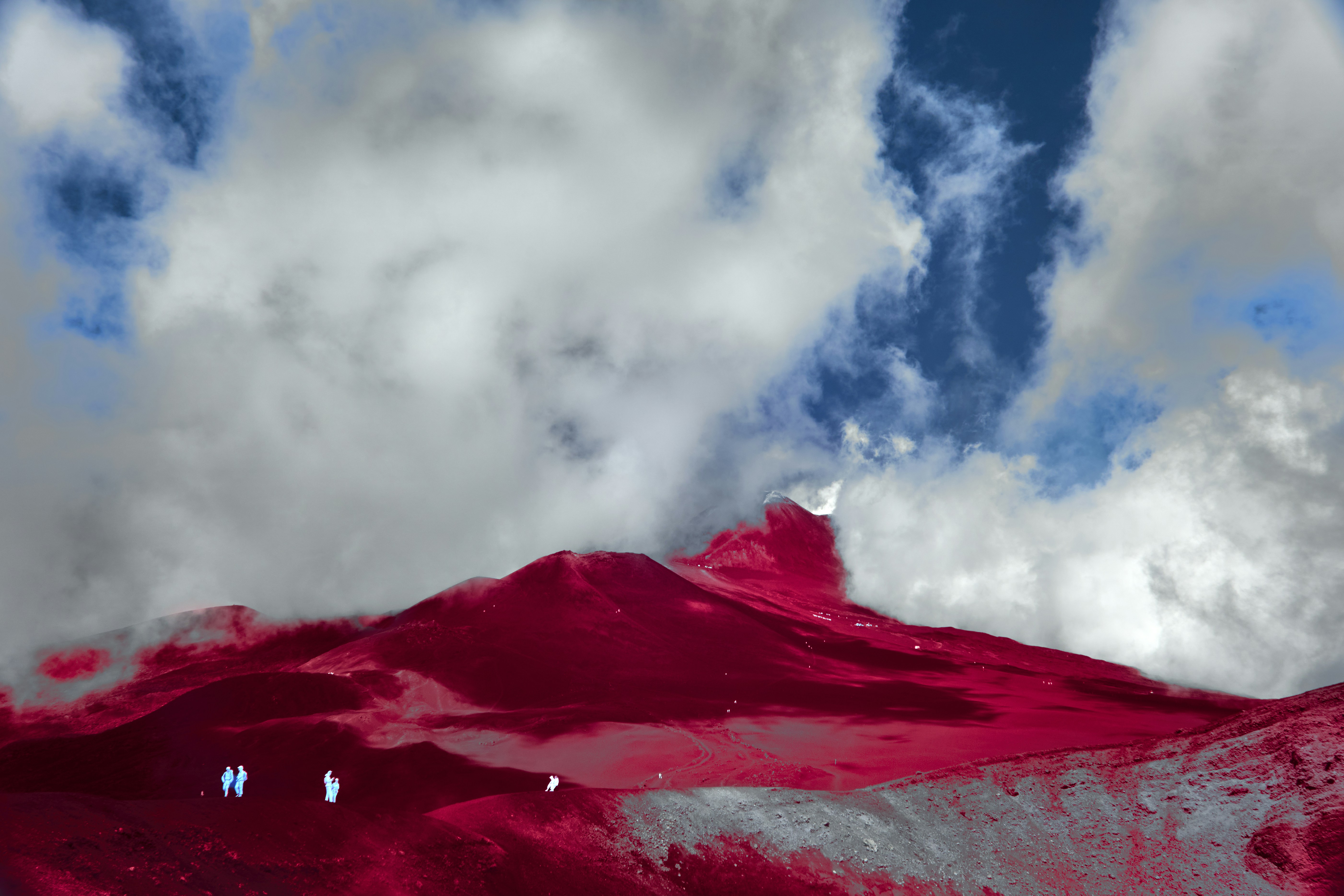 Ätna in infrarot bei 720nm | People hike on a vibrant red mountain under clouds.