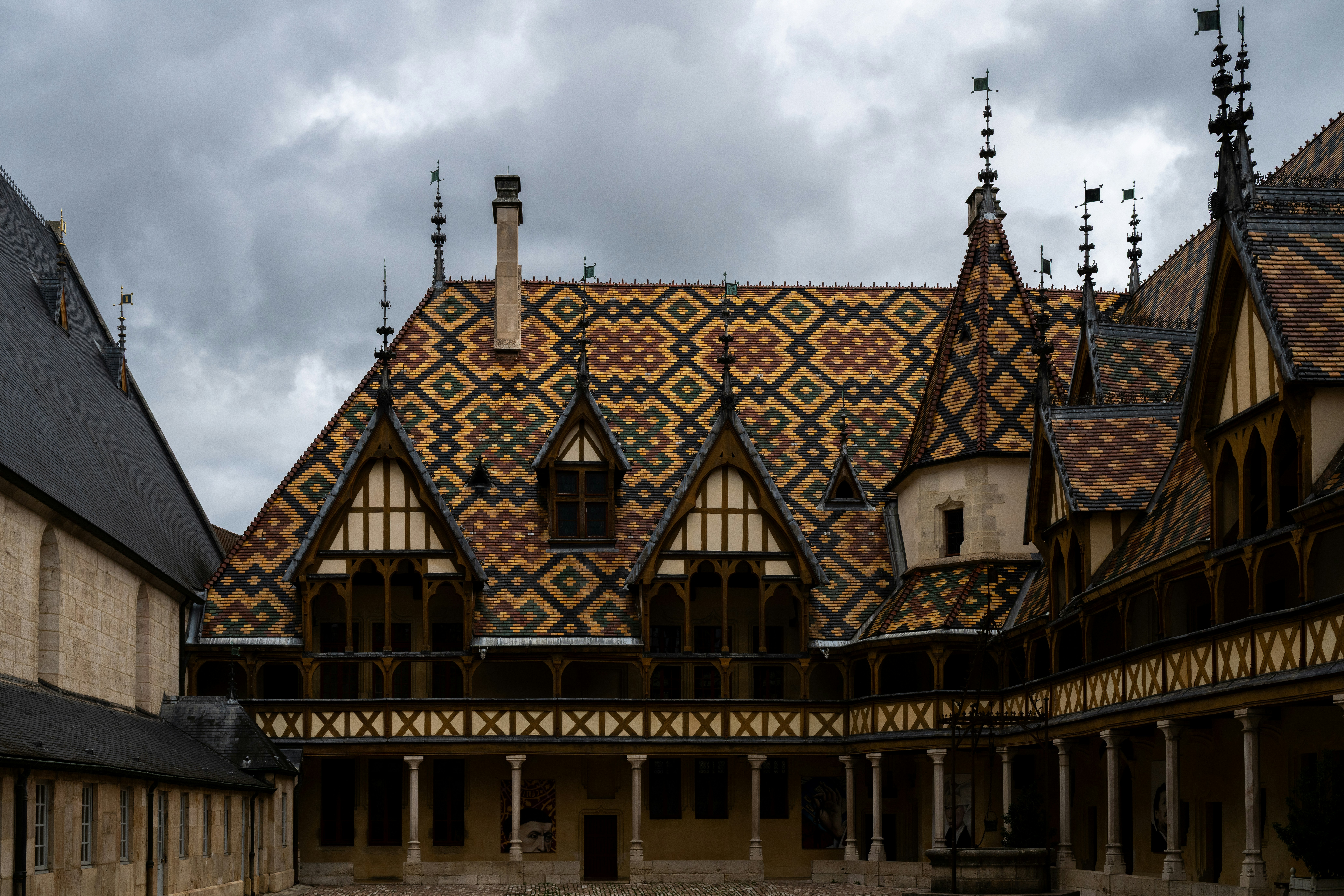 Colorful patterned rooftops of a historical building in Burgundy, framed by a dramatic sky.