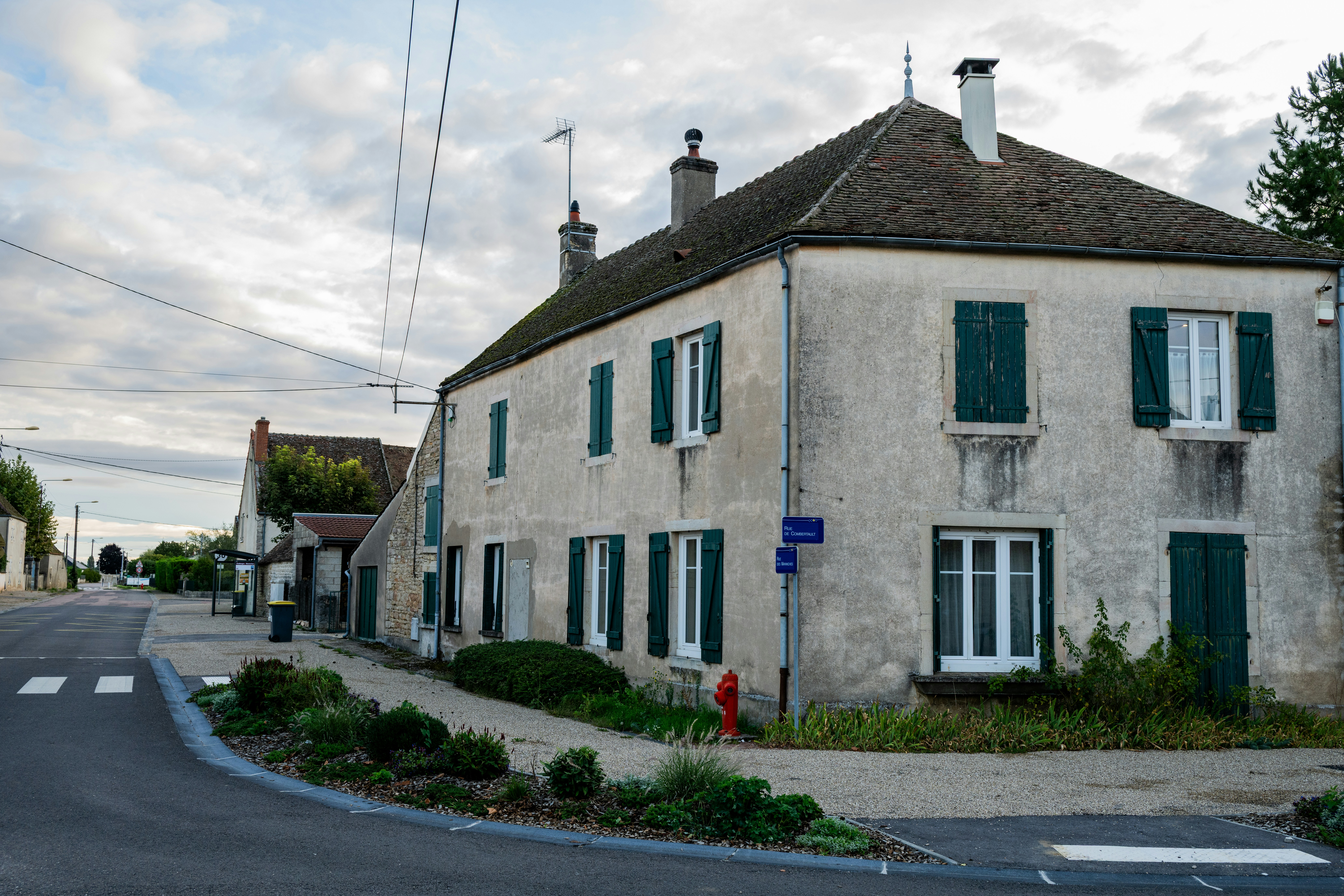 A two-story house with green shutters on a street.
