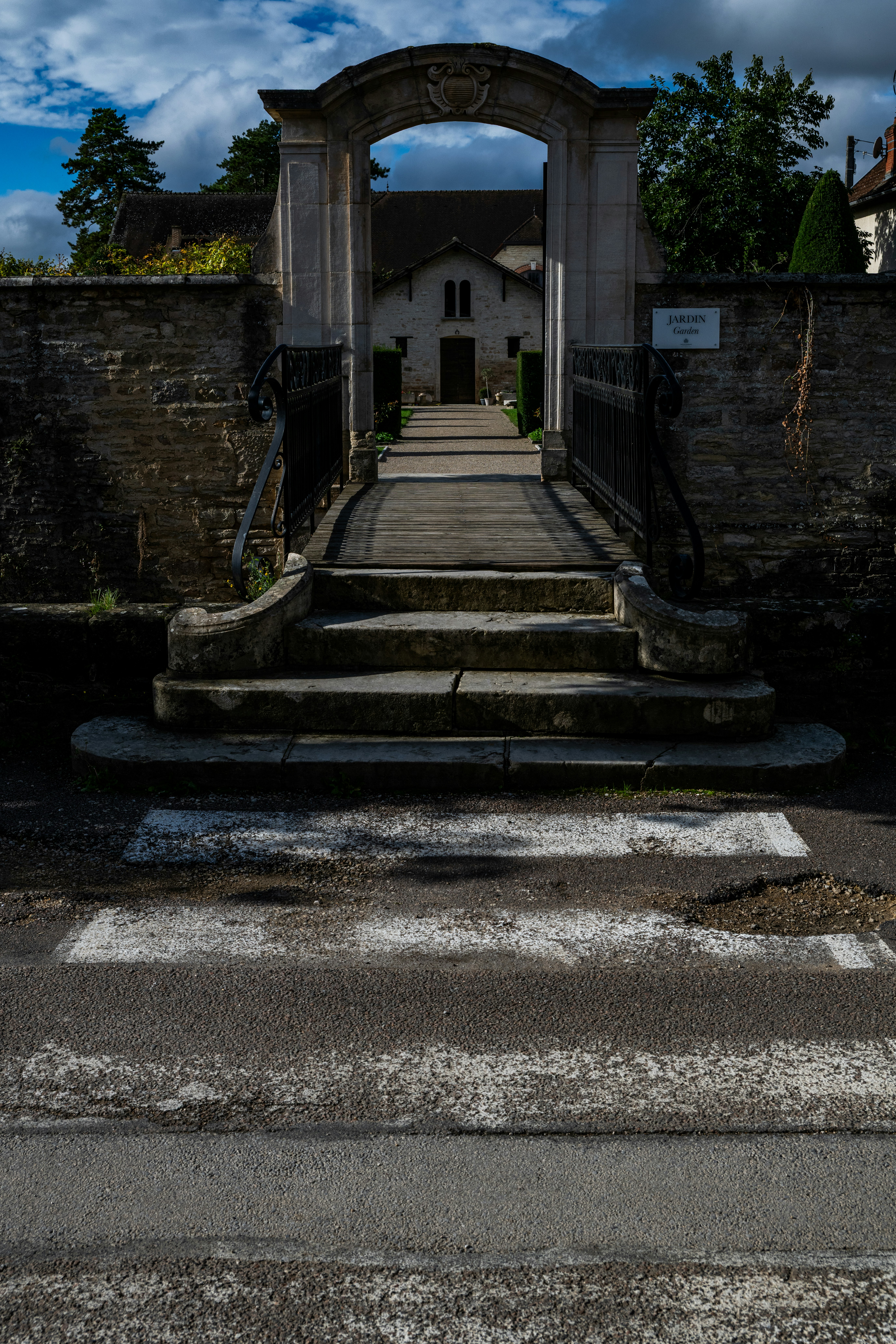 Stone archway leading to a serene garden path, framed by lush greenery and historical architecture.