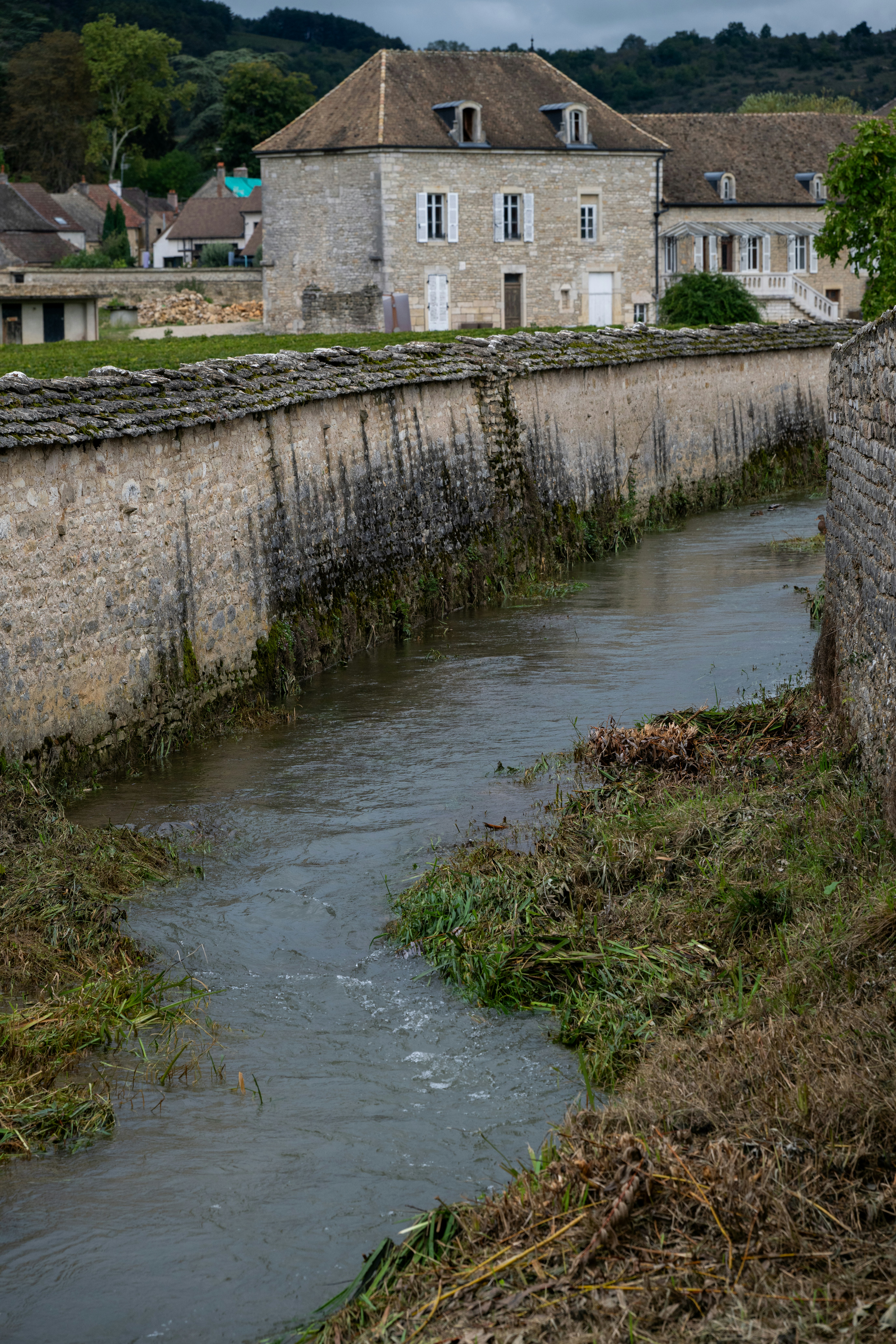 Stone buildings beside a flowing stream with vegetation.