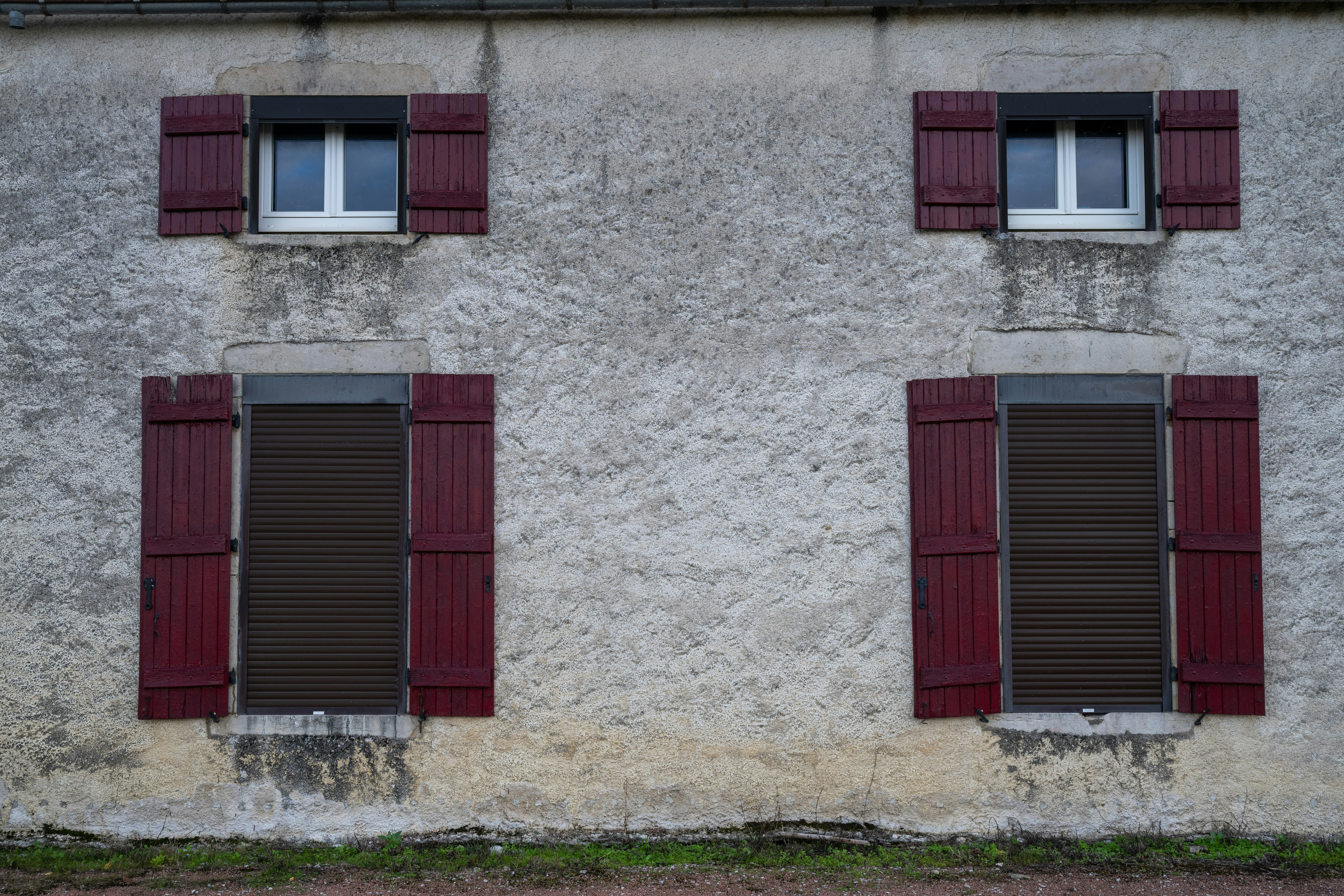Four windows with red shutters on a textured wall