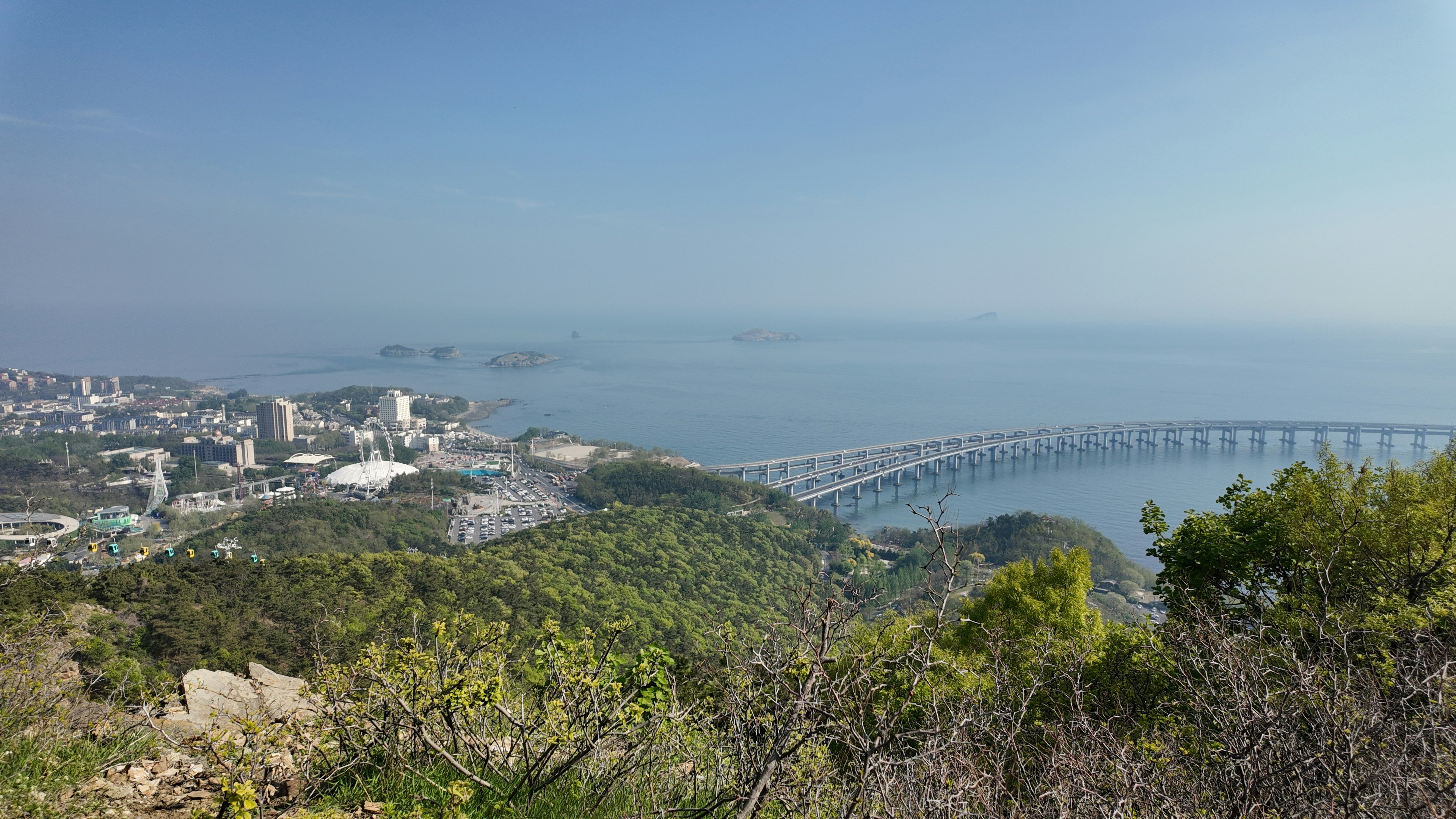 Cityscape with bridge over the ocean and green hills.