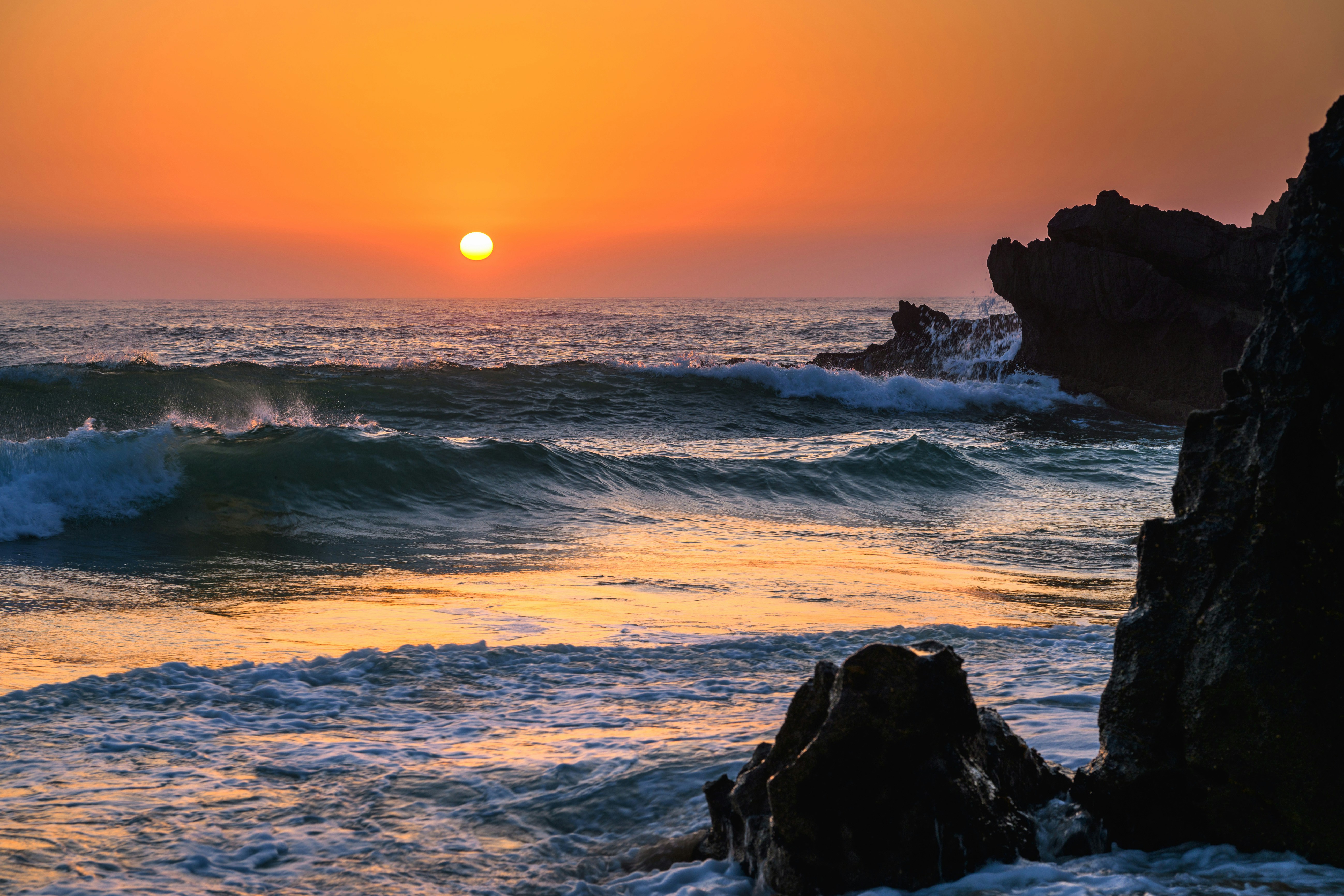 Sunset over the ocean with waves crashing on rocks