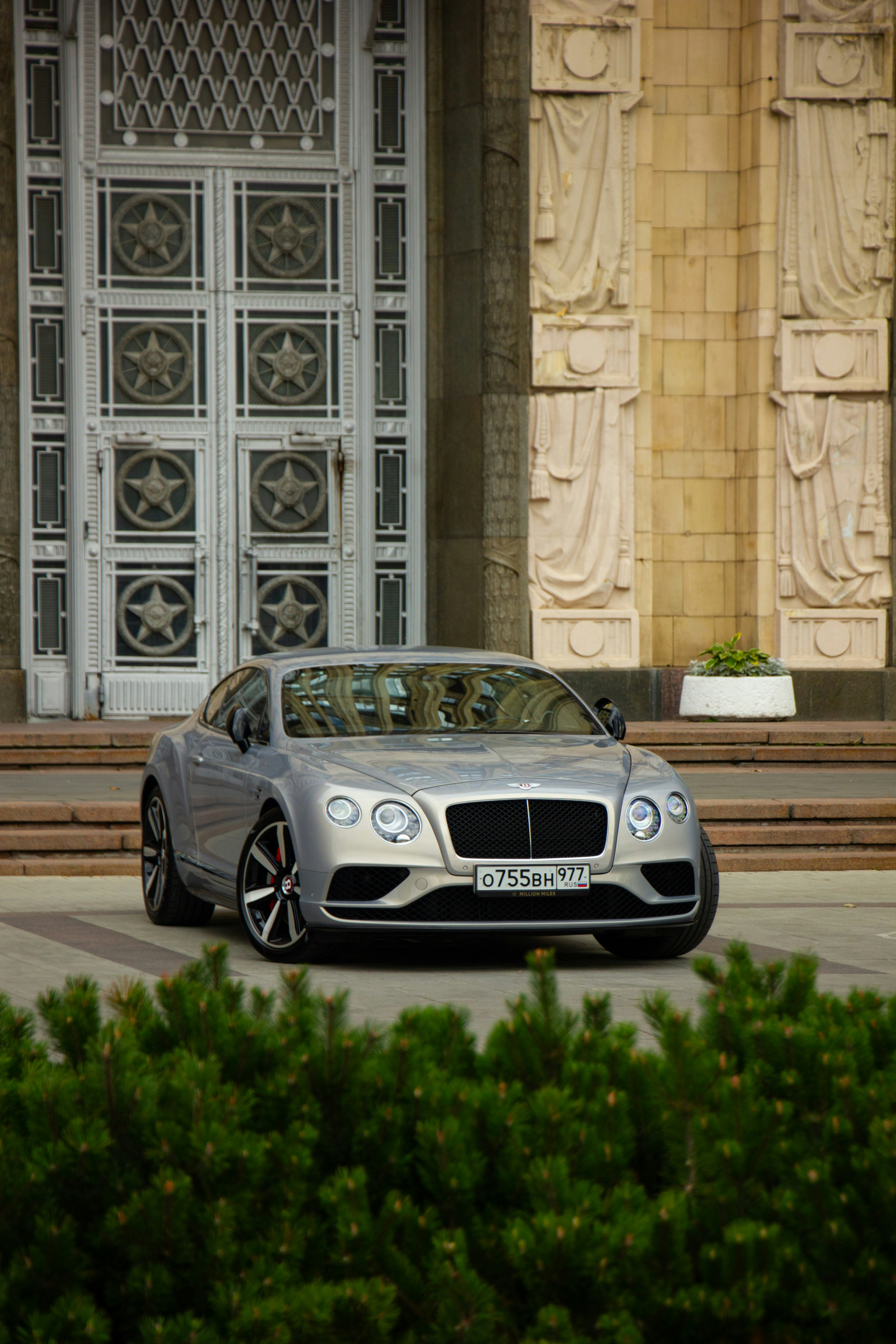 Sleek silver sports car parked in front of a grand architectural backdrop, highlighted by intricate stonework and an ornate entrance.