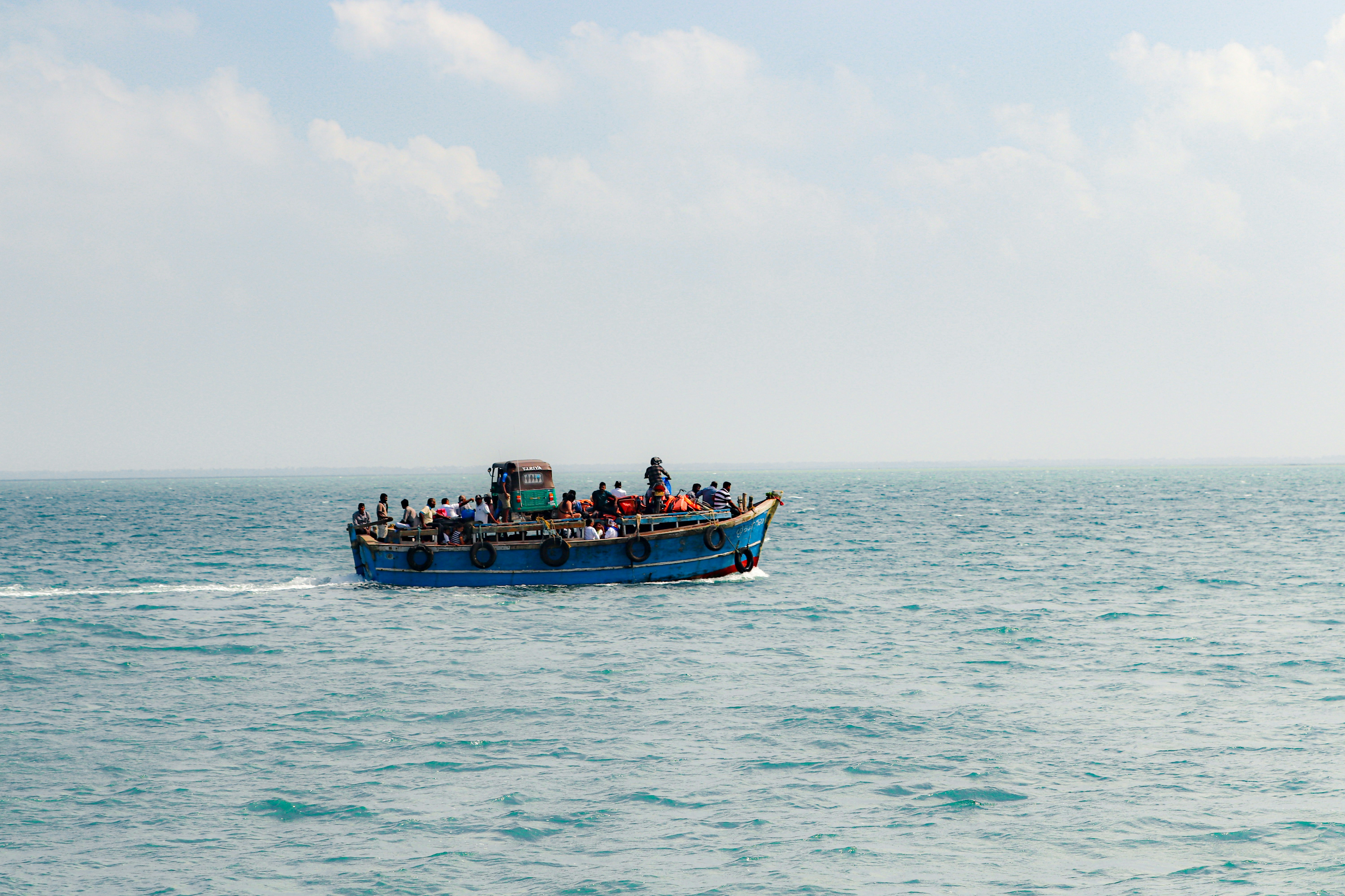 A blue boat with many people sails on the ocean.