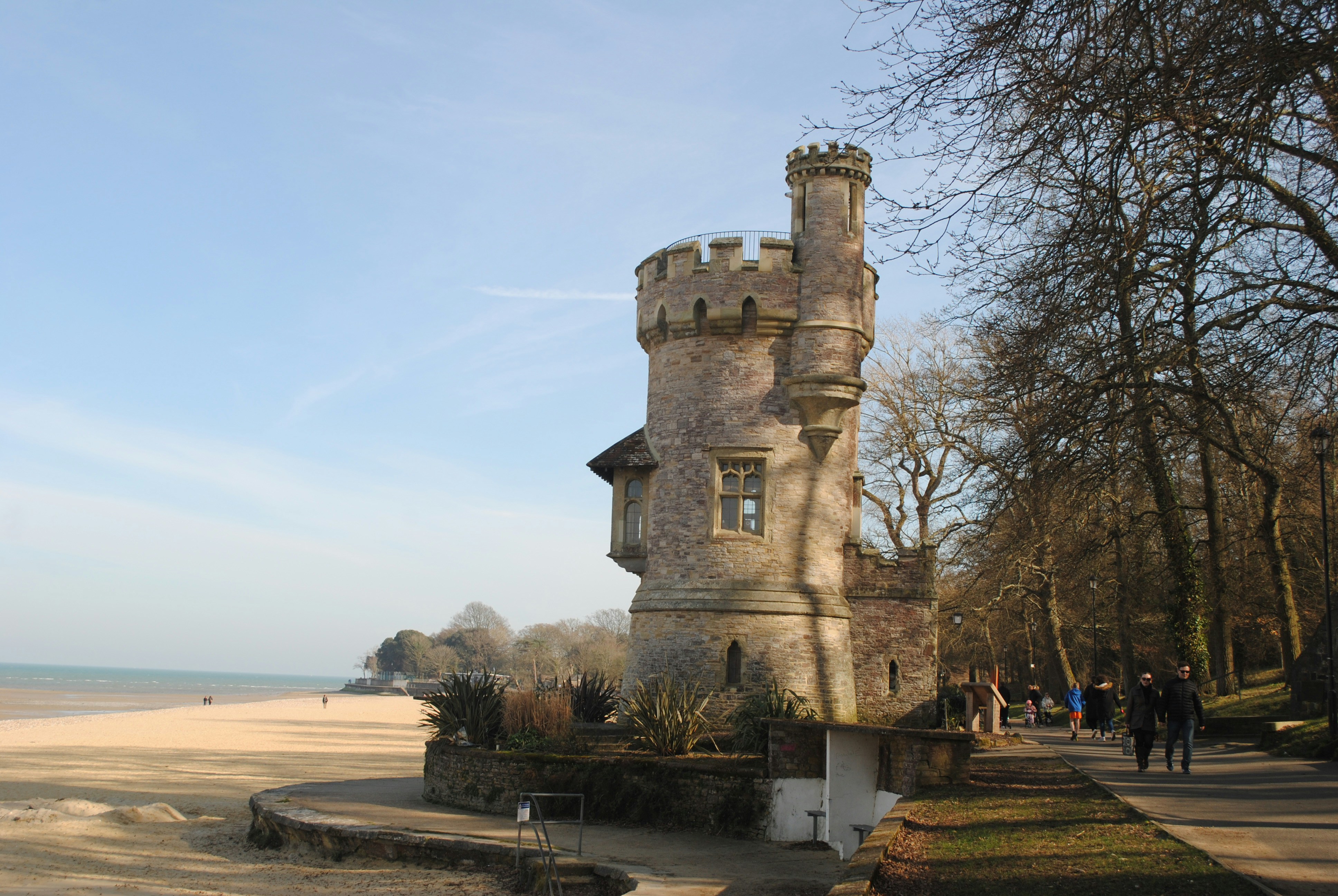 Stone tower on a beach with trees and people.