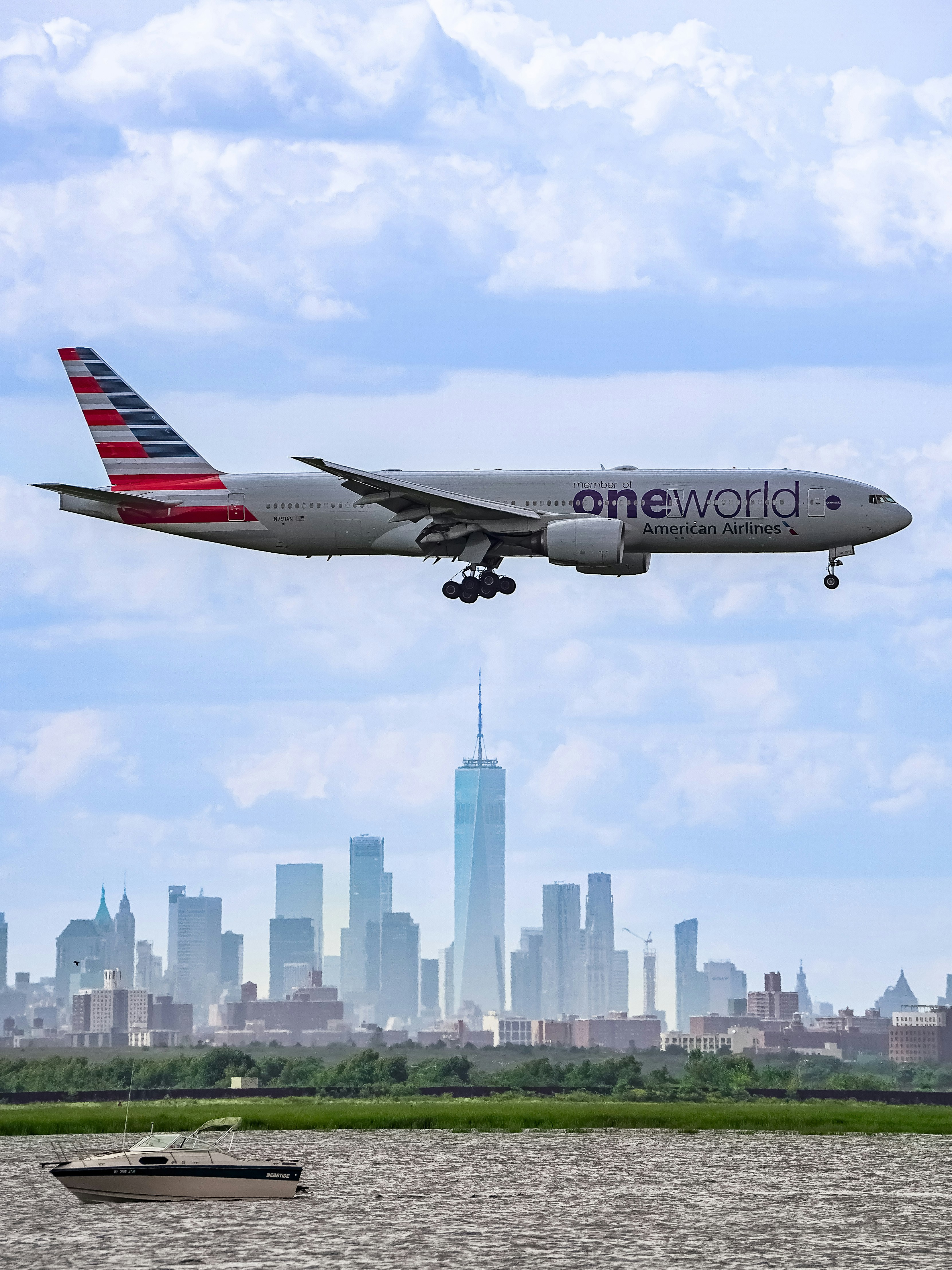 American Airlines plane descending towards the skyline of New York City, with a boat in the foreground. The scene captures a moment of urban life and aviation.