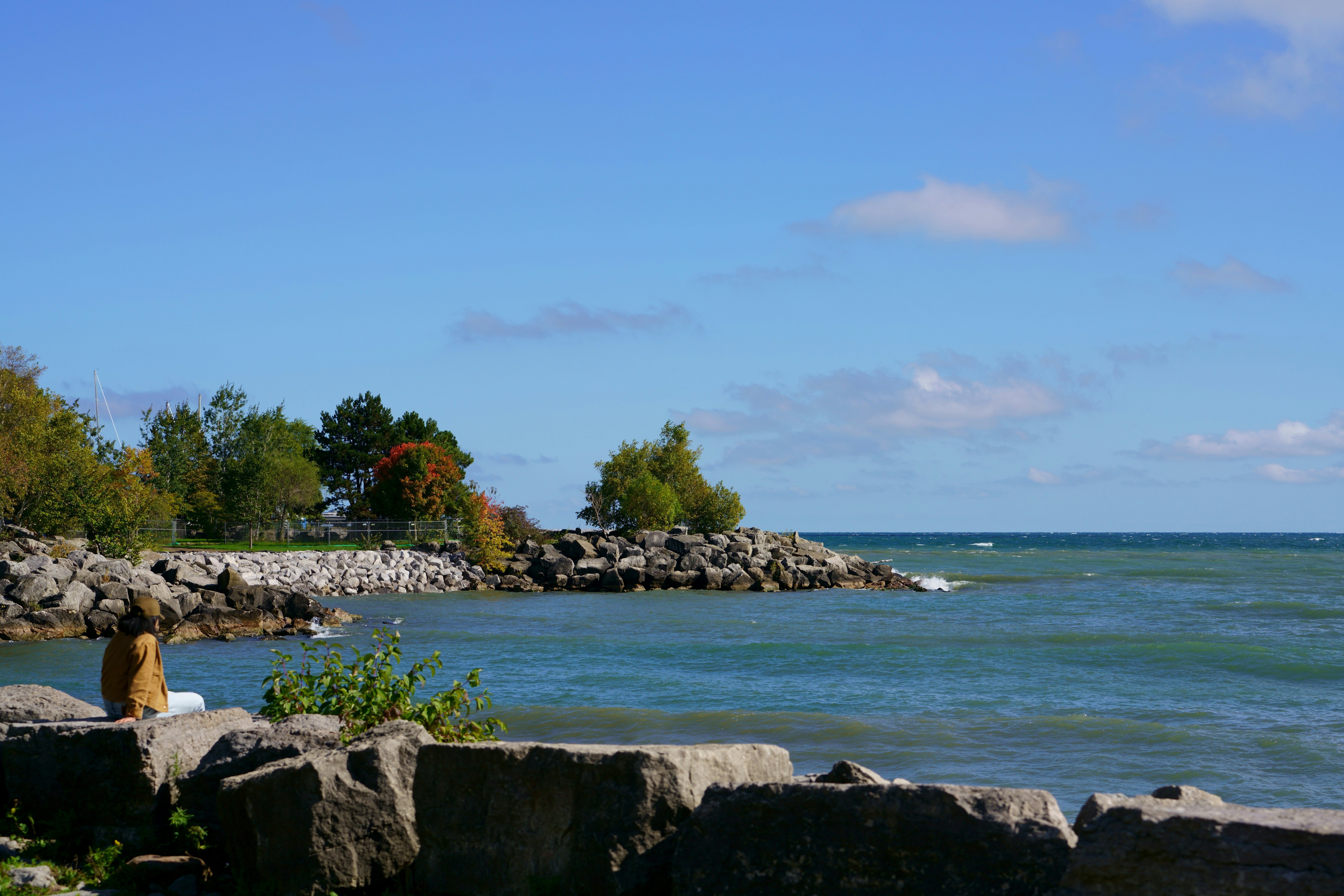 A person sits on rocks overlooking a calm blue lake.