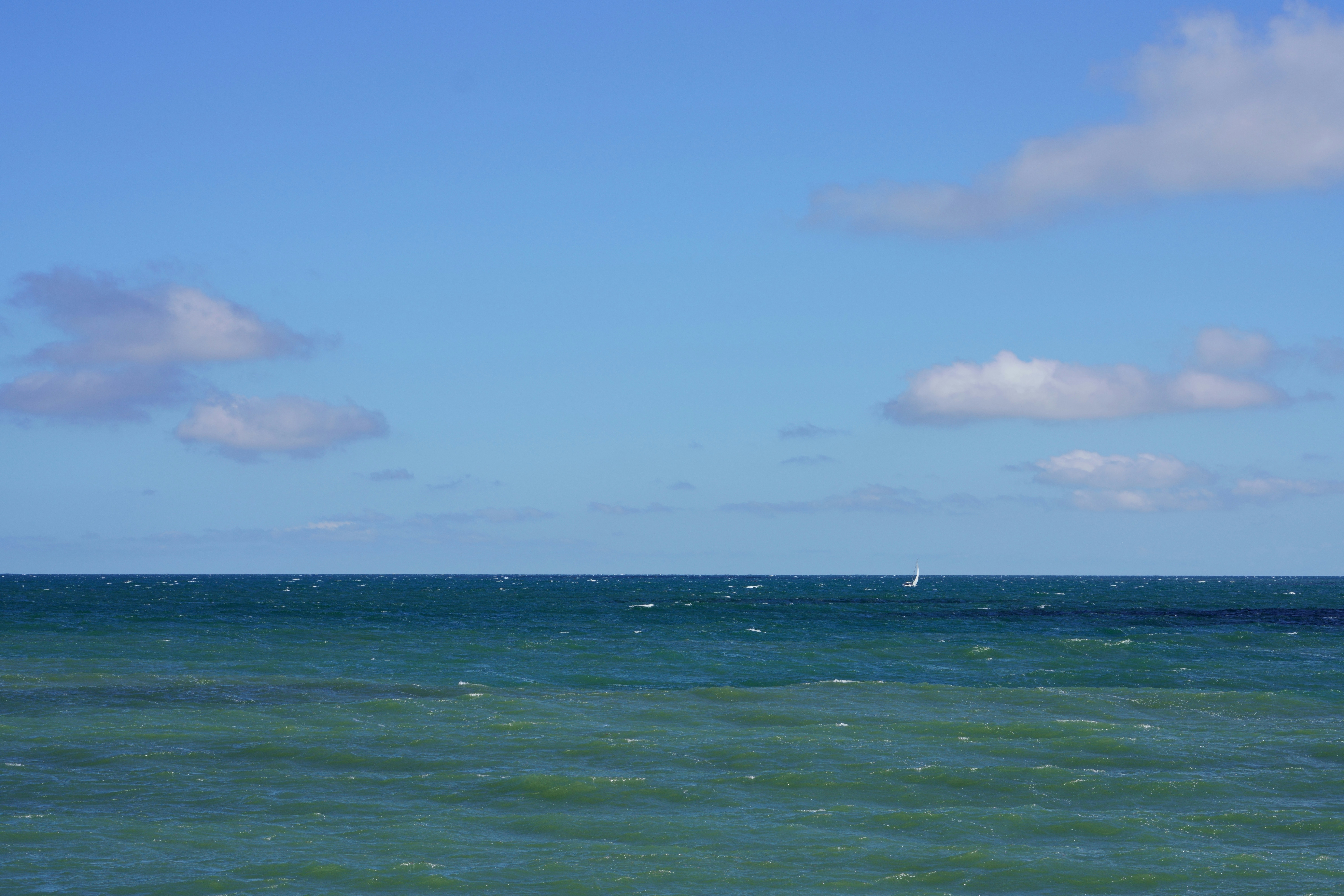 Two sailboats on a choppy turquoise ocean under blue sky.