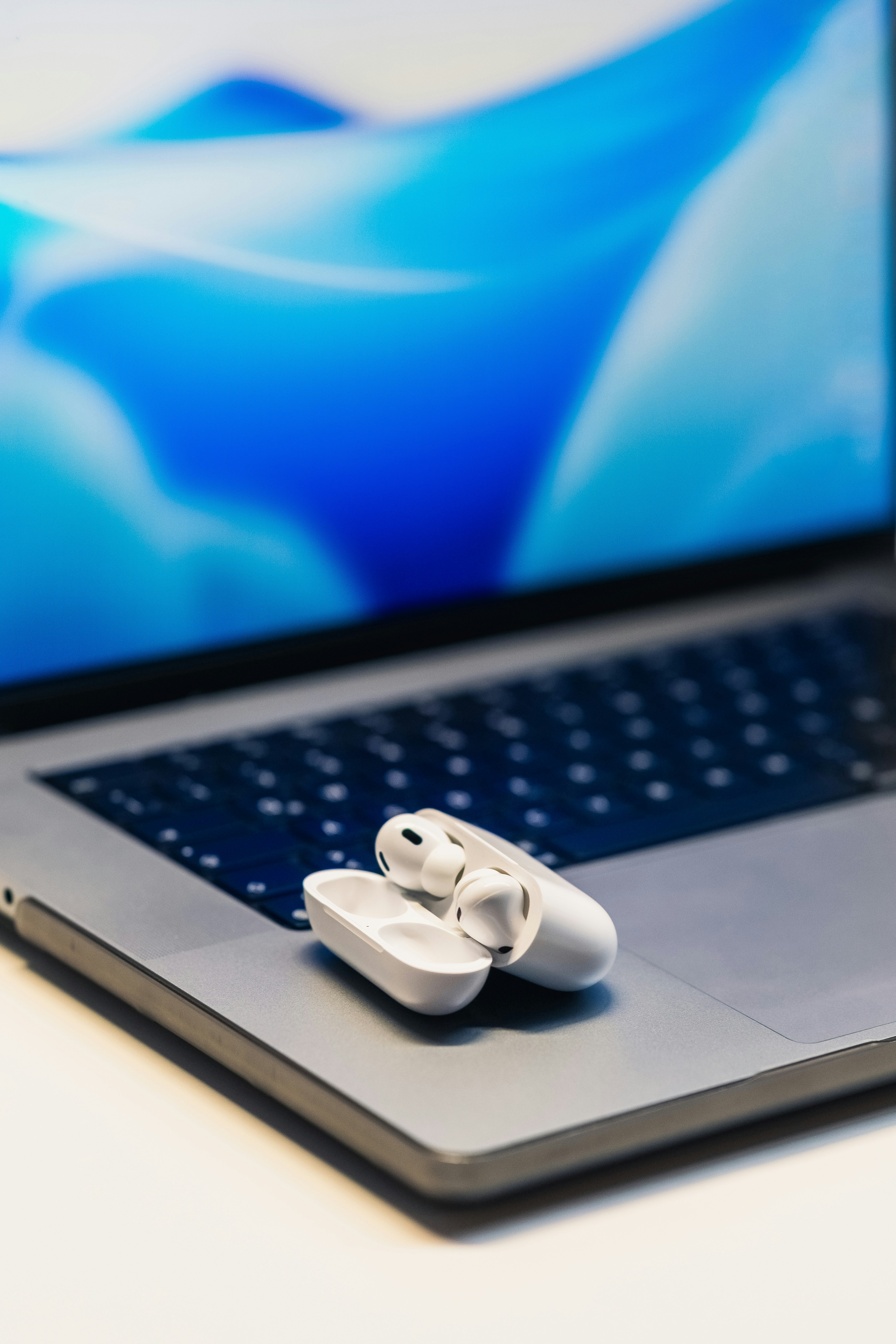 Wireless earbuds resting on a sleek laptop keyboard, with a vibrant abstract background displayed on the screen.