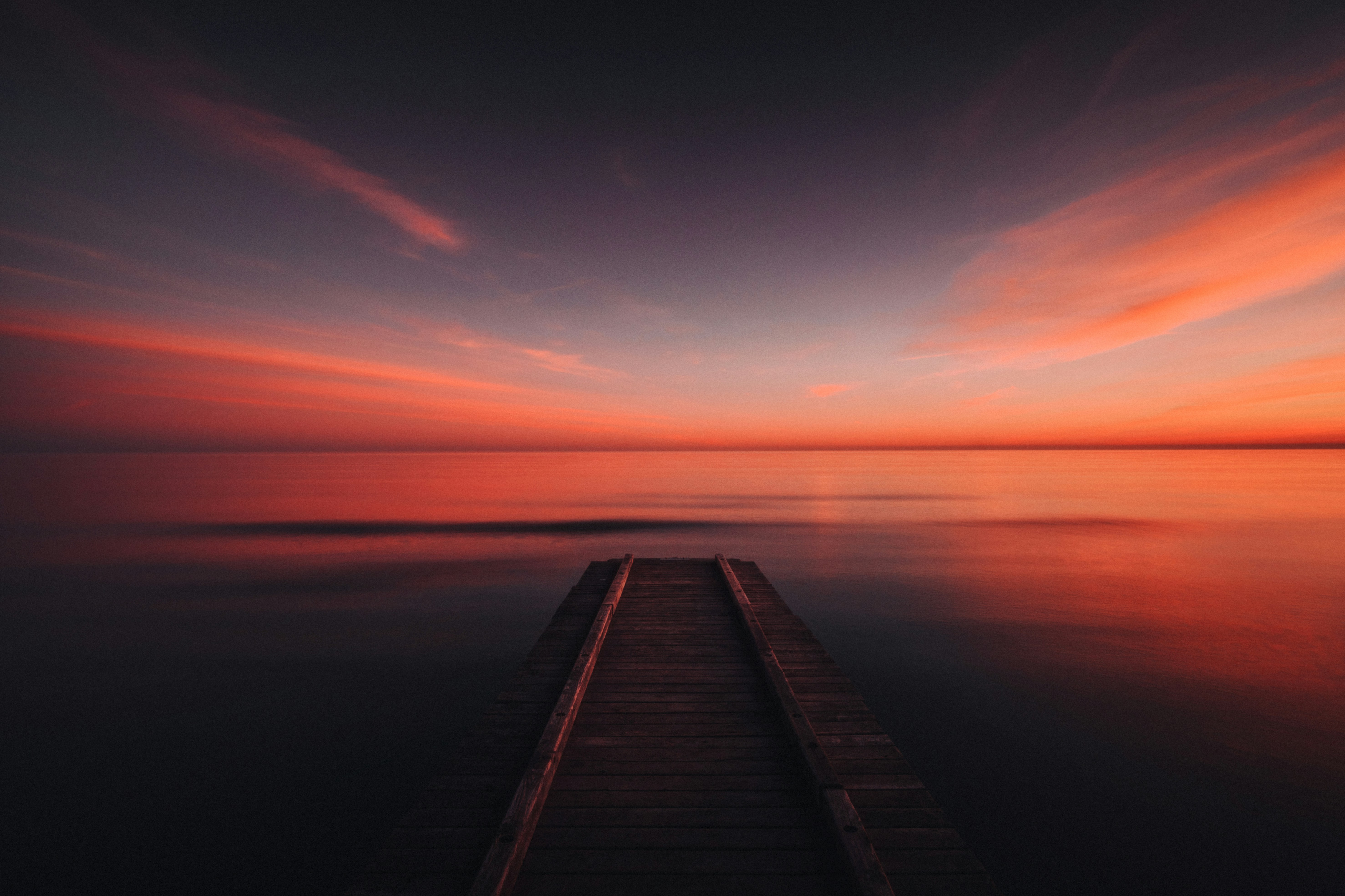 Wooden pier extending into calm ocean at sunset