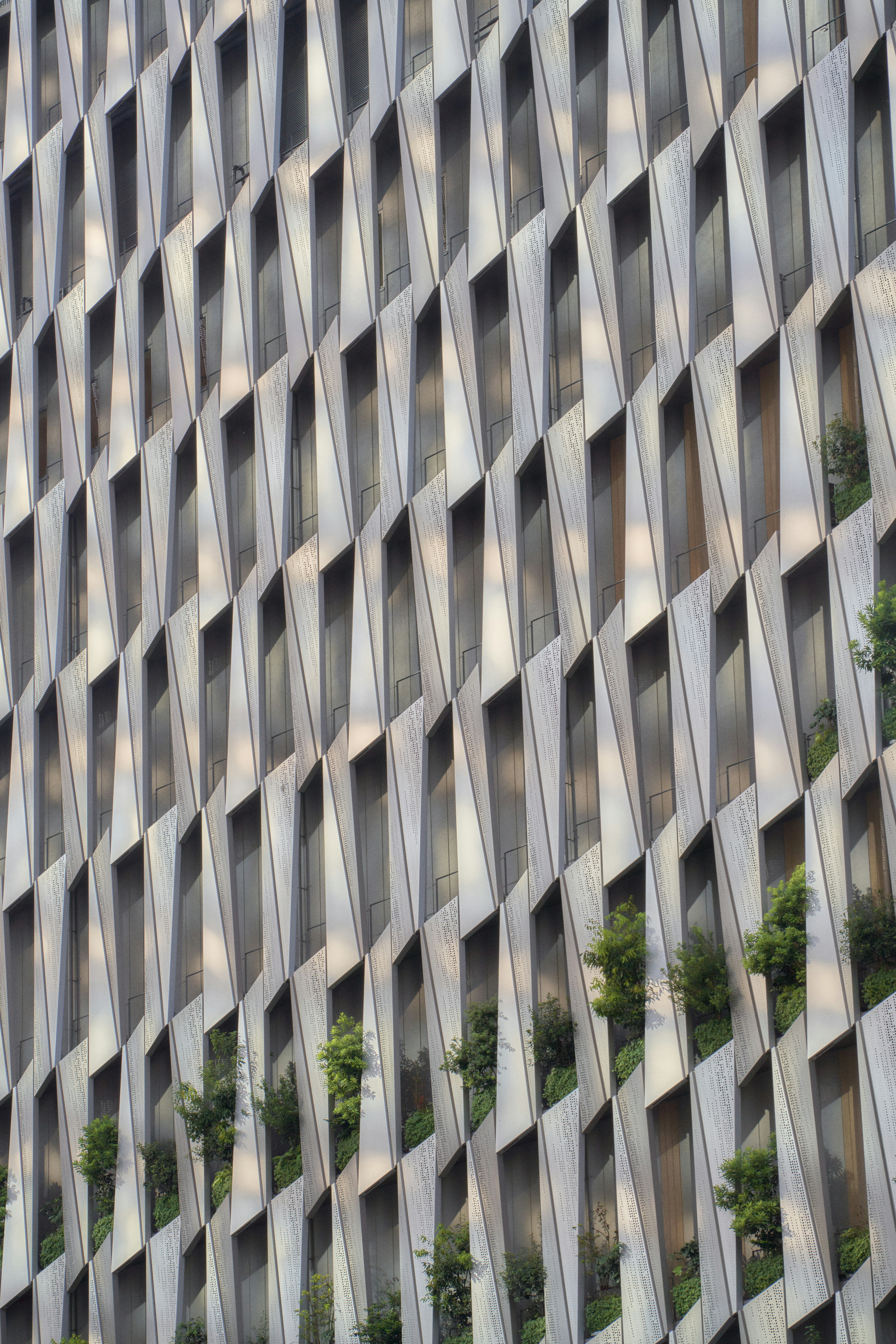 Intricate facade of a modern building featuring diamond-shaped windows and greenery integrated into the architecture.