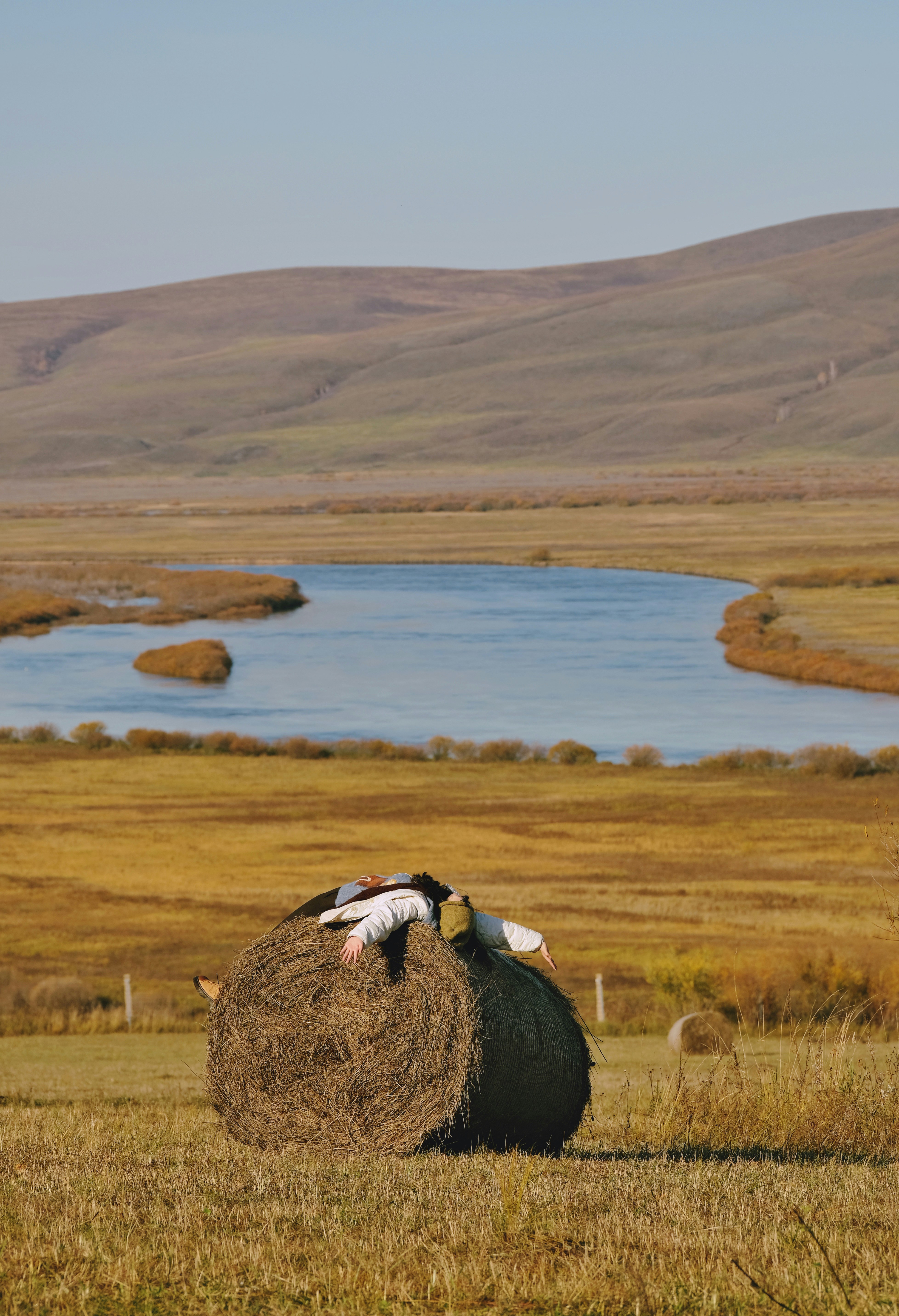 Resting on a hay bale beneath the autumn sun. | People resting on hay bales in a field.